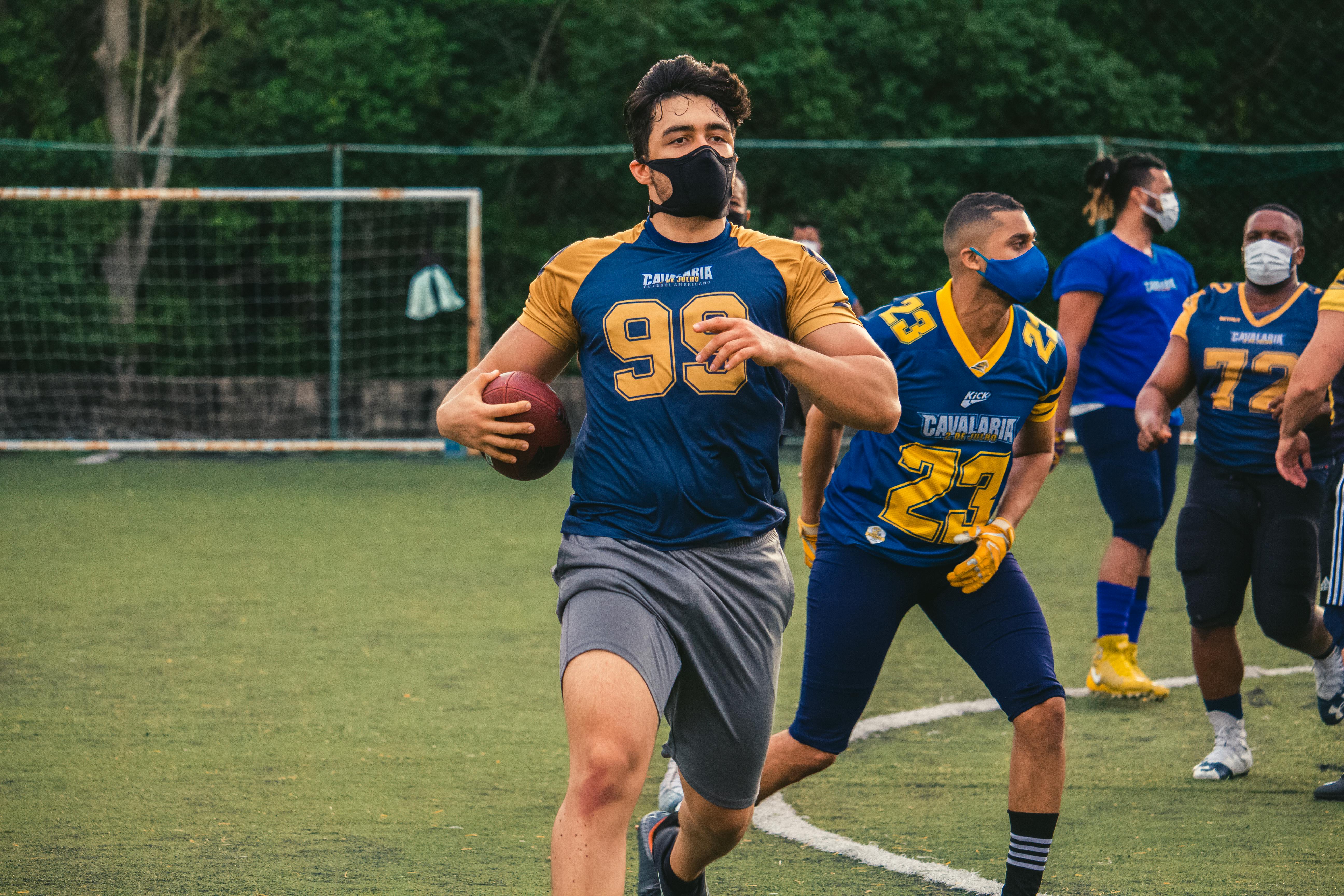 A Man Wearing a Face Mask Running with a Rugby Ball · Free Stock Photo
