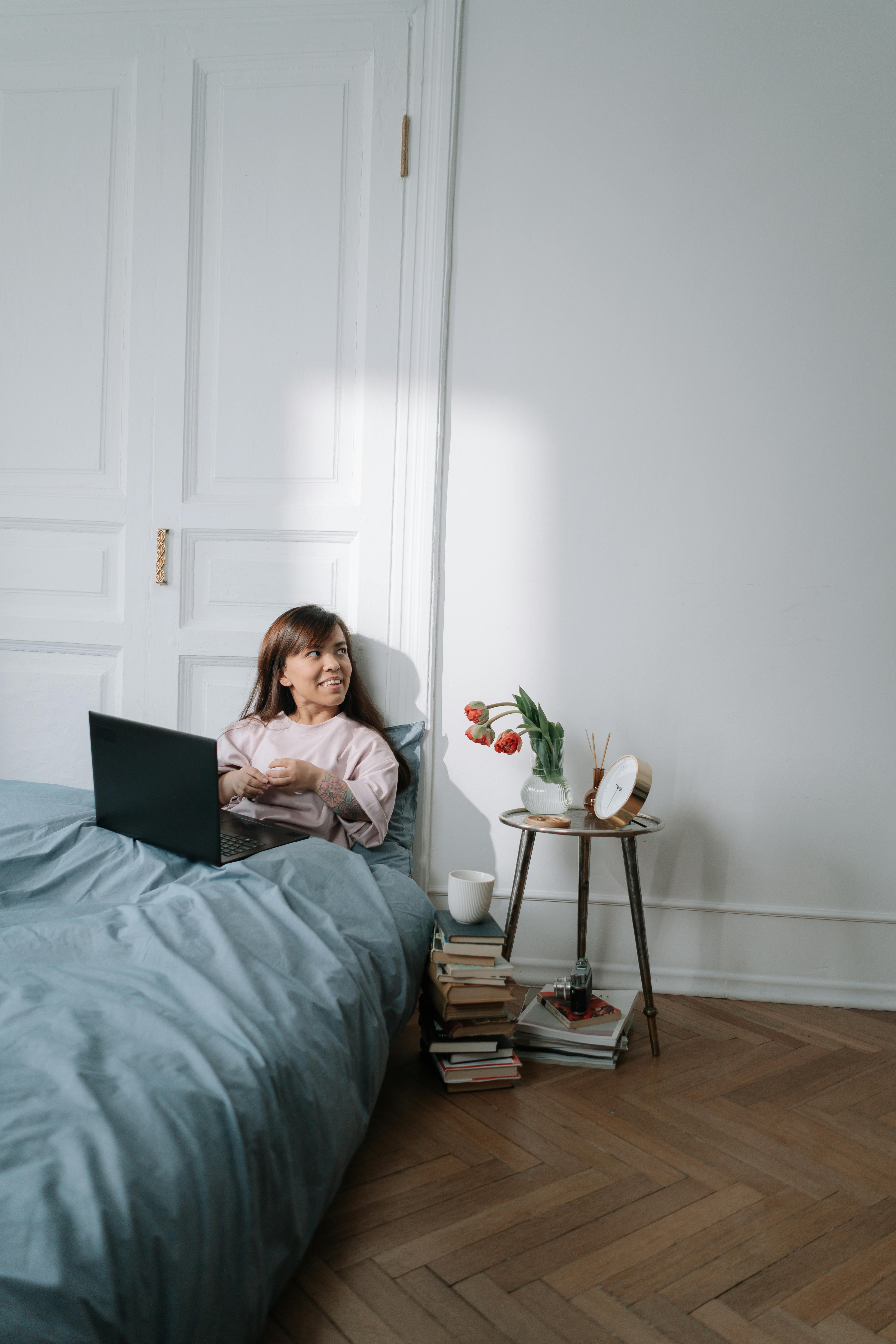 Dwarf girl sitting in bed with open laptop and smiling · Free Stock Photo