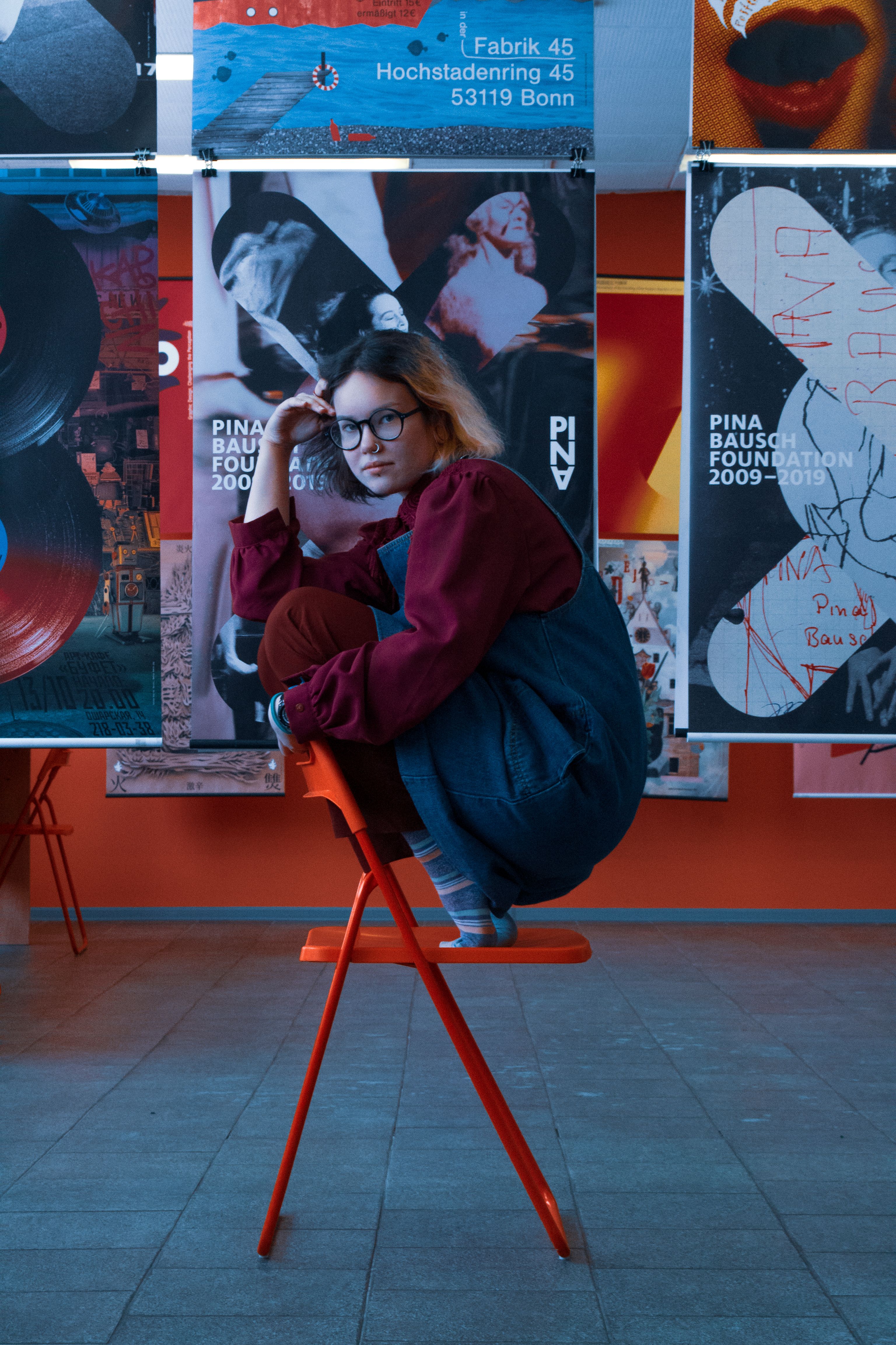 Woman Wearing Eyeglasses Crouching on a Folding Chair · Free Stock Photo