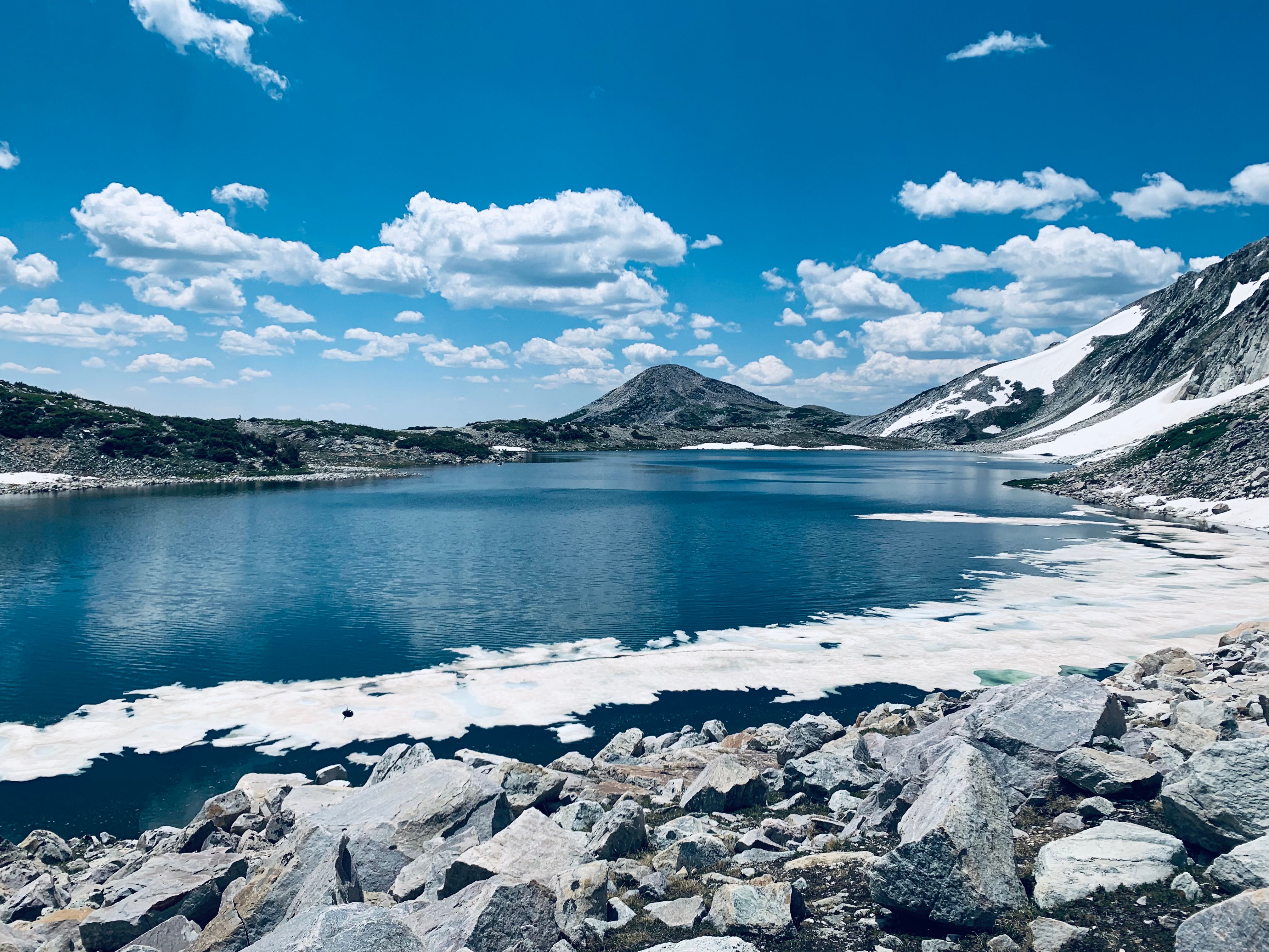 Gray Rocky Shore Across Blue Lake Under Blue and White Cloudy Sky ...