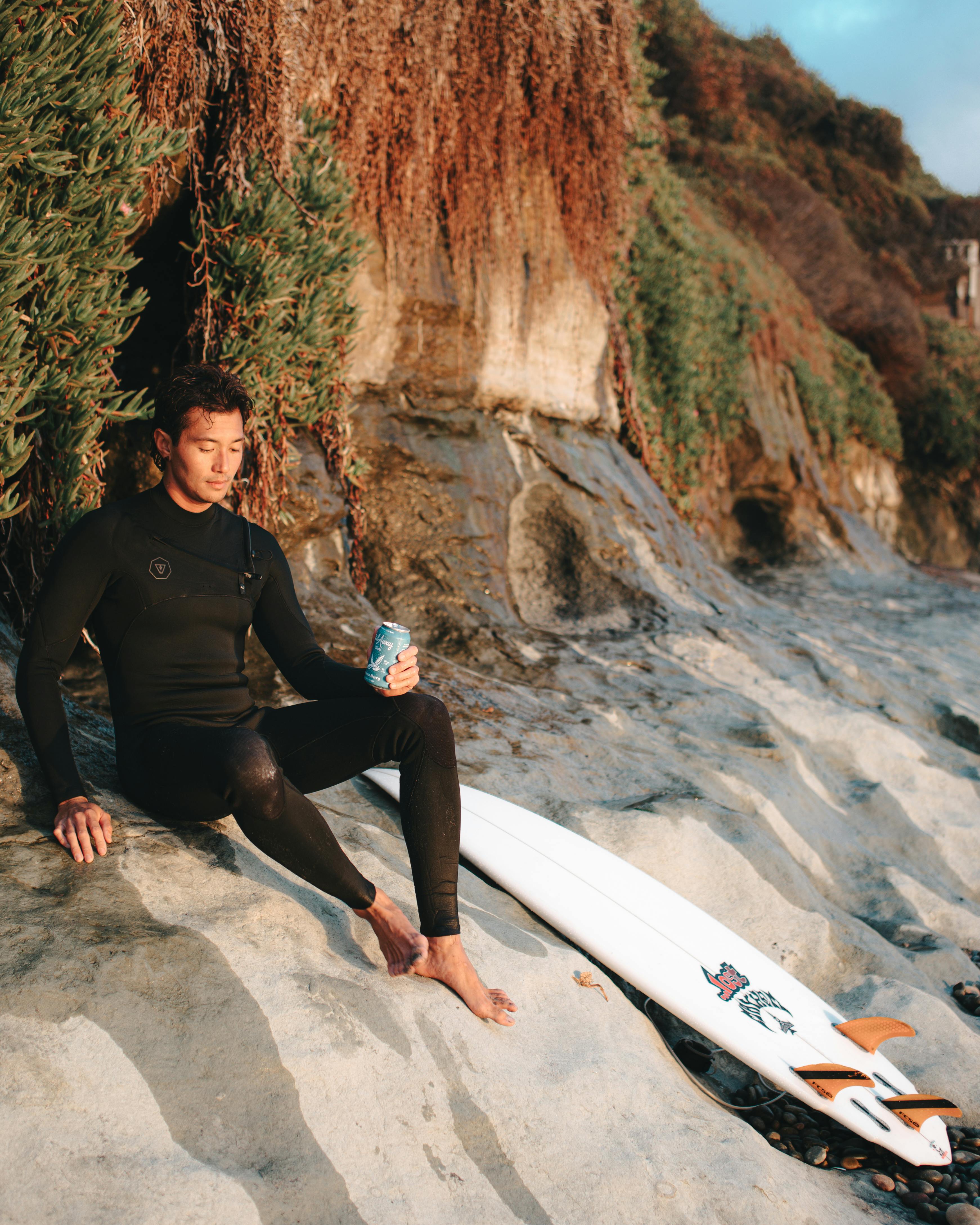 Man in Black Wetsuit Sitting on a Rock Beside a White Surfboard · Free ...