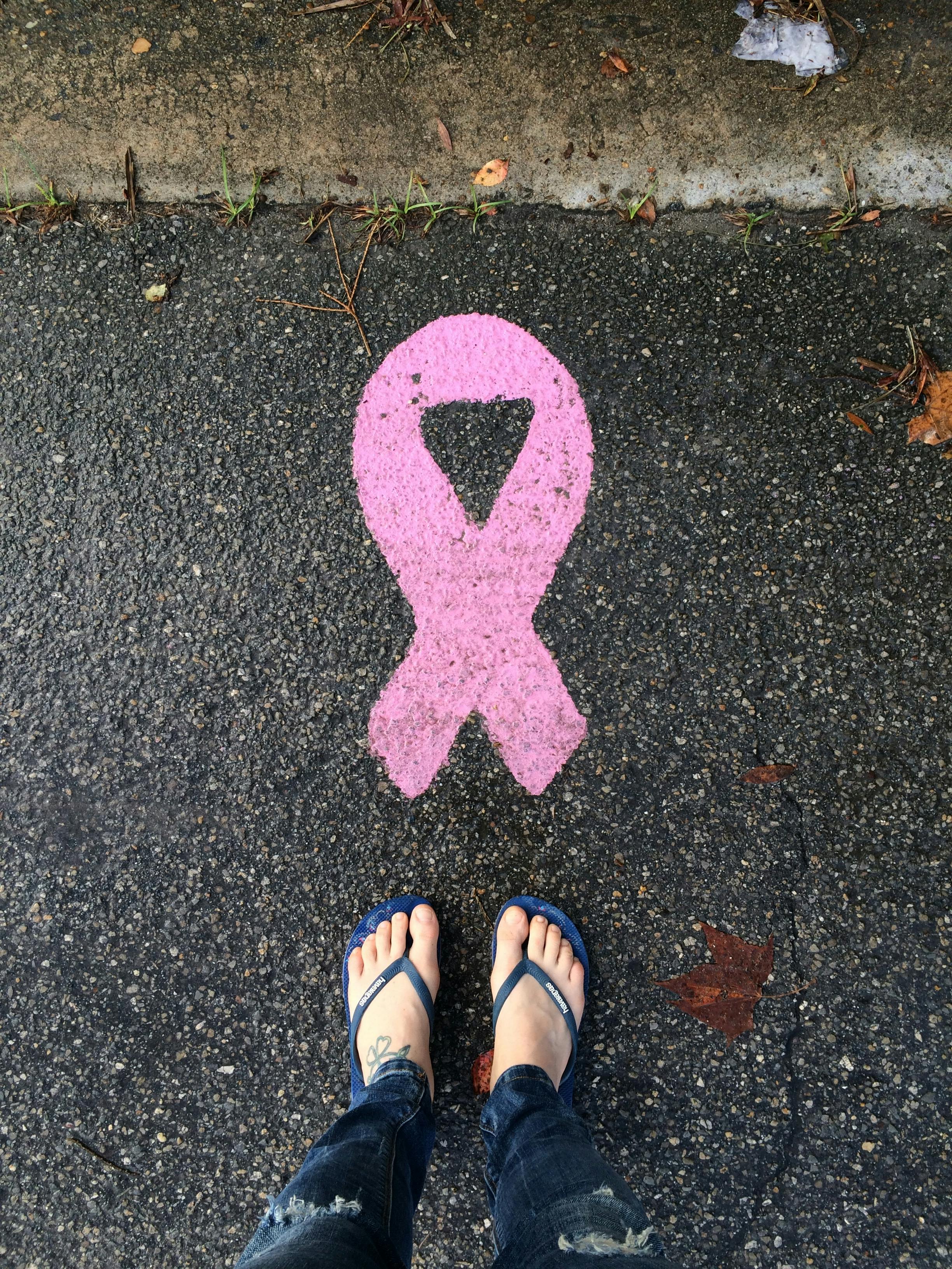 Person Legs near Cancer Awareness Pink Ribbon on Asphalt · Free Stock Photo
