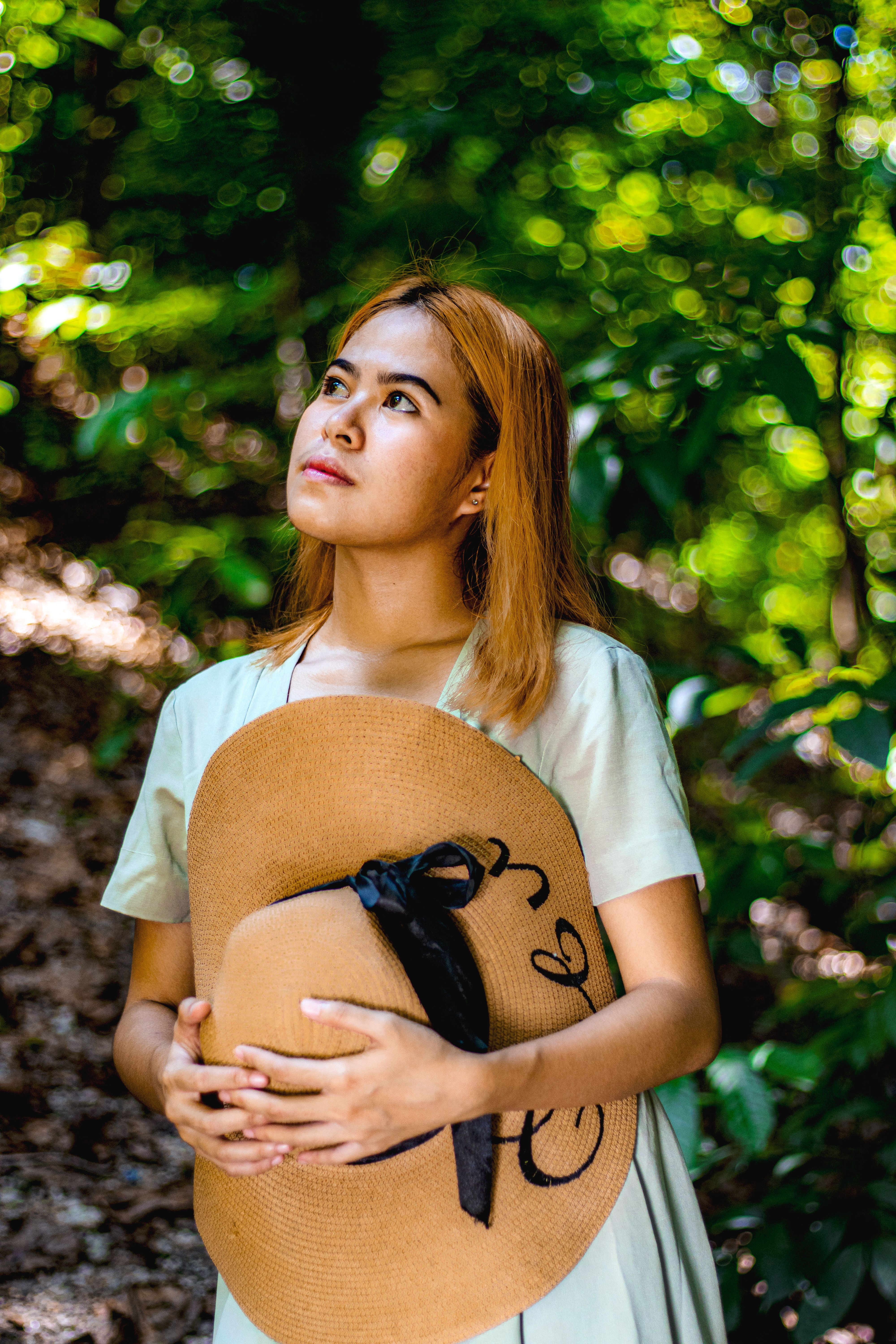 Woman Hugging a Sun Hat while Looking Up · Free Stock Photo