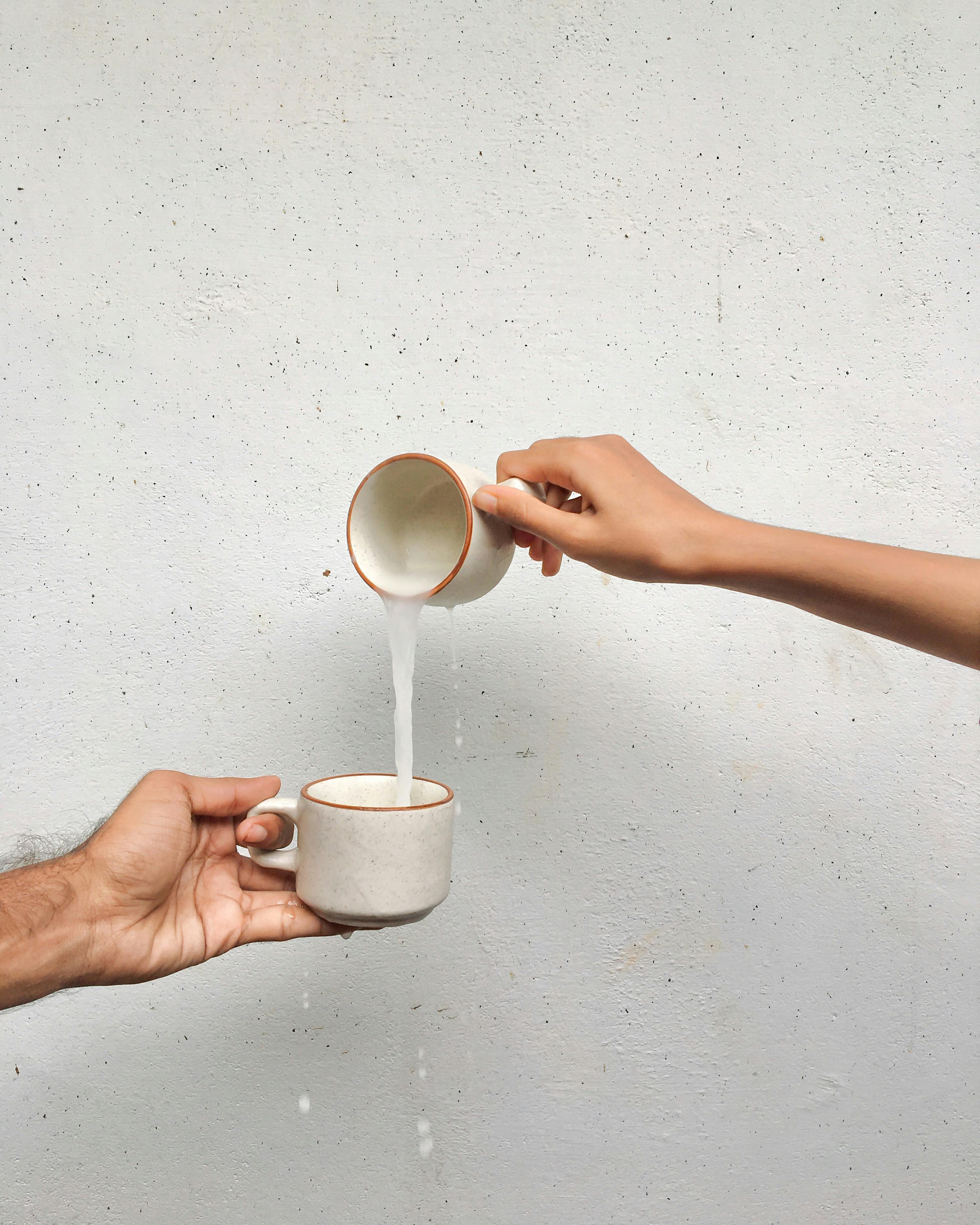 Person Pouring White Liquid on a Ceramic Cup · Free Stock Photo