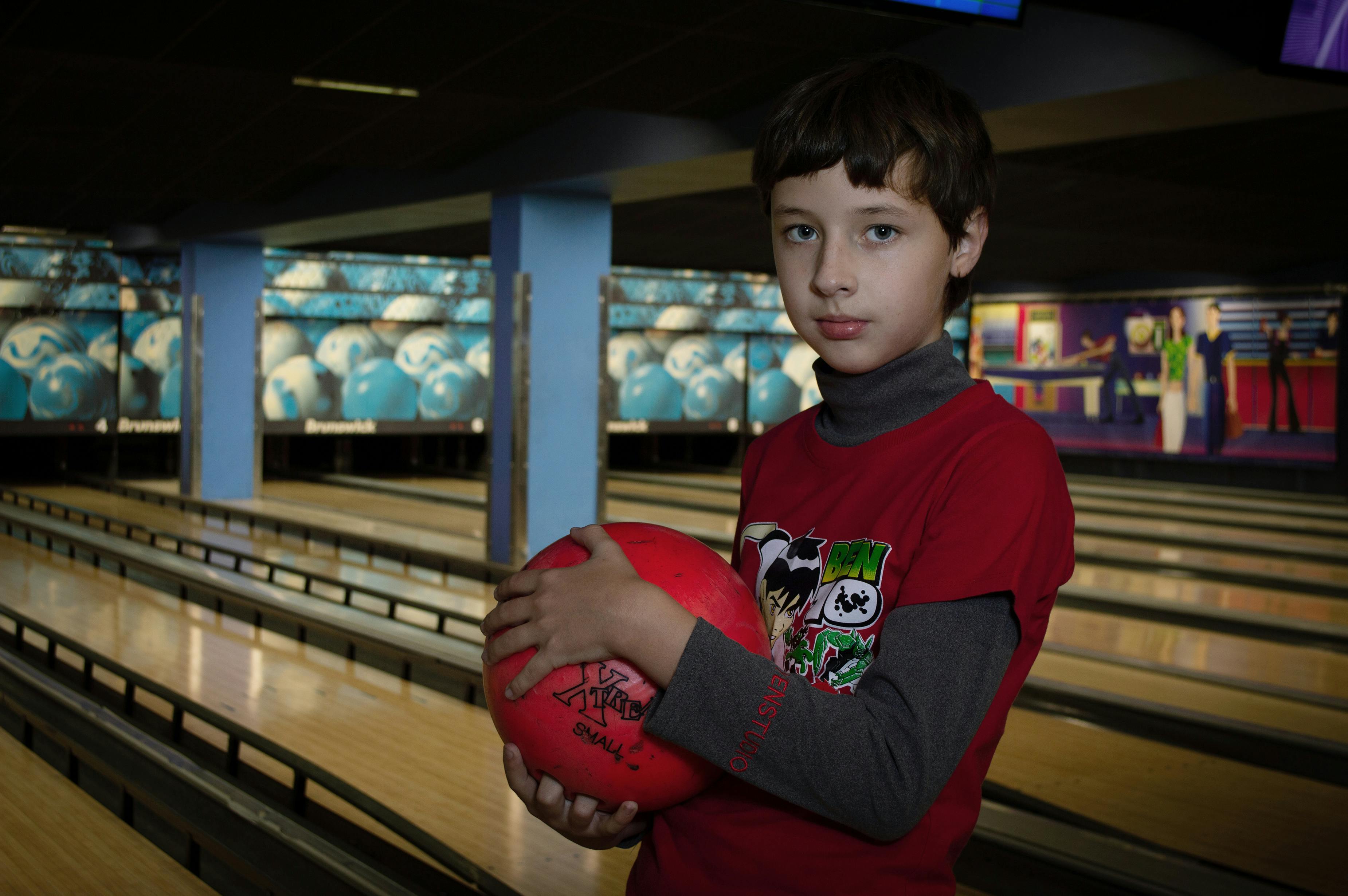 A Serious Boy Holding a Red Bowling Ball · Free Stock Photo