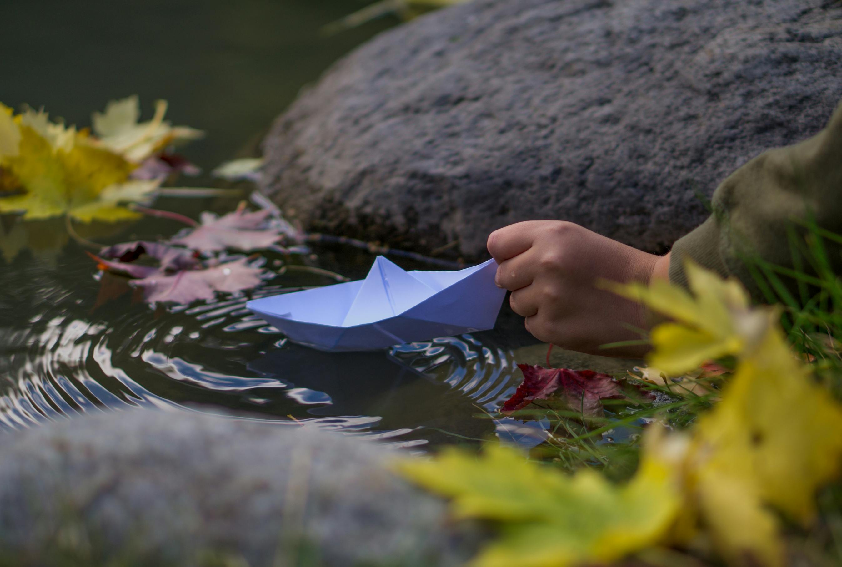 A Hand Putting the Paper Boat on the Water · Free Stock Photo