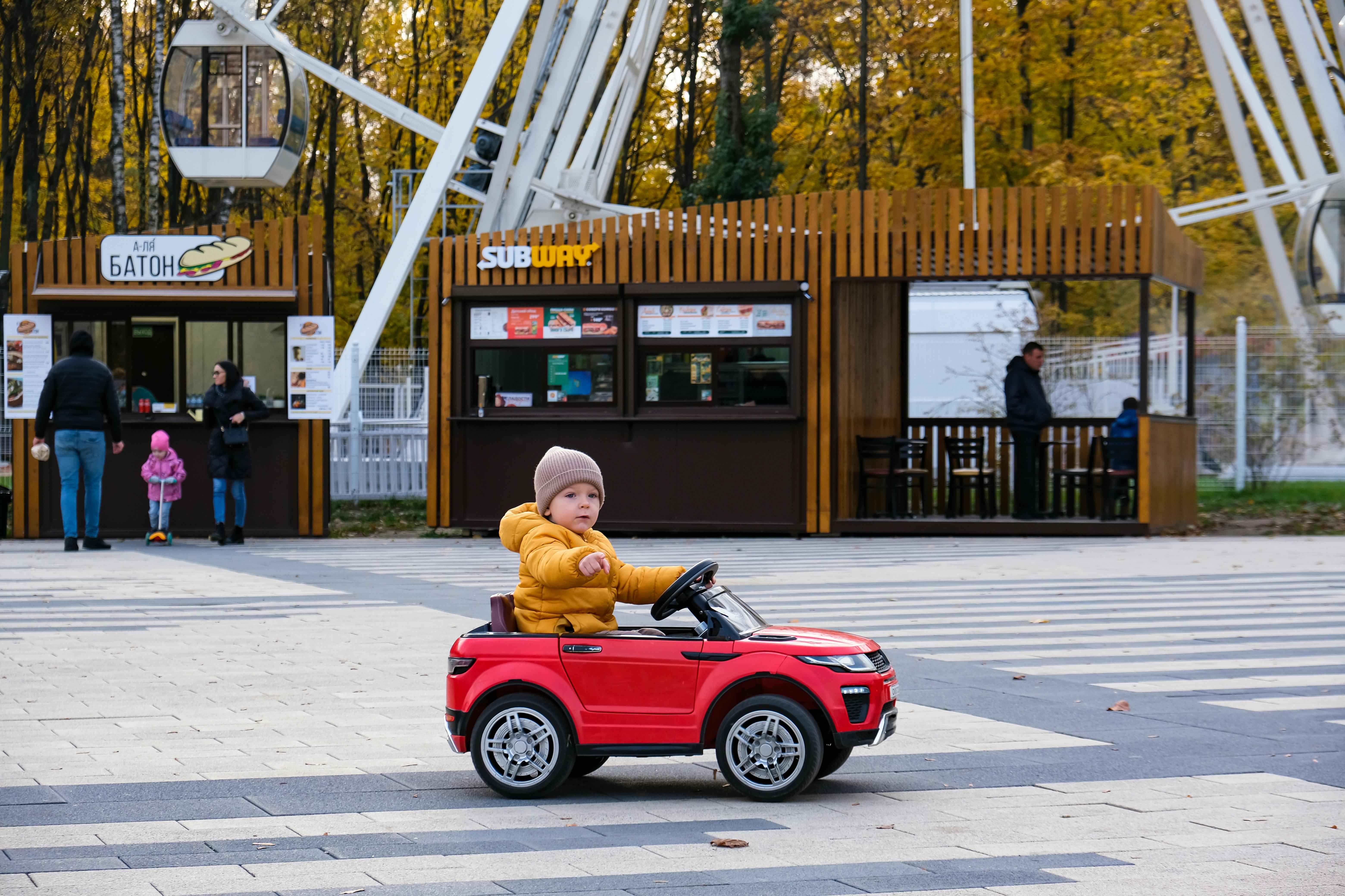 A Child Riding a Toy Car in the Street · Free Stock Photo