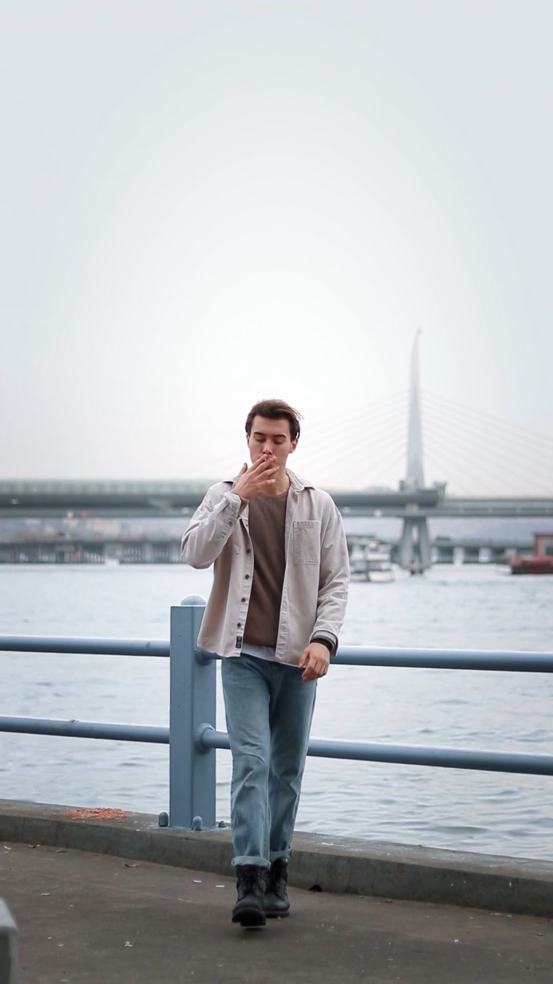 A Young Man Smoking a Cigarette while Walking by a Body of Water Free ...