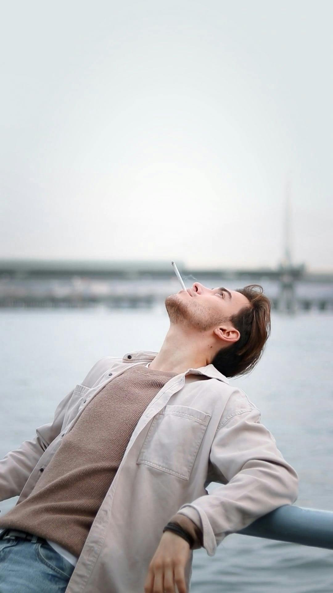 A Young Man Smoking a Cigarette while Leaning on a Metal Railing Free ...