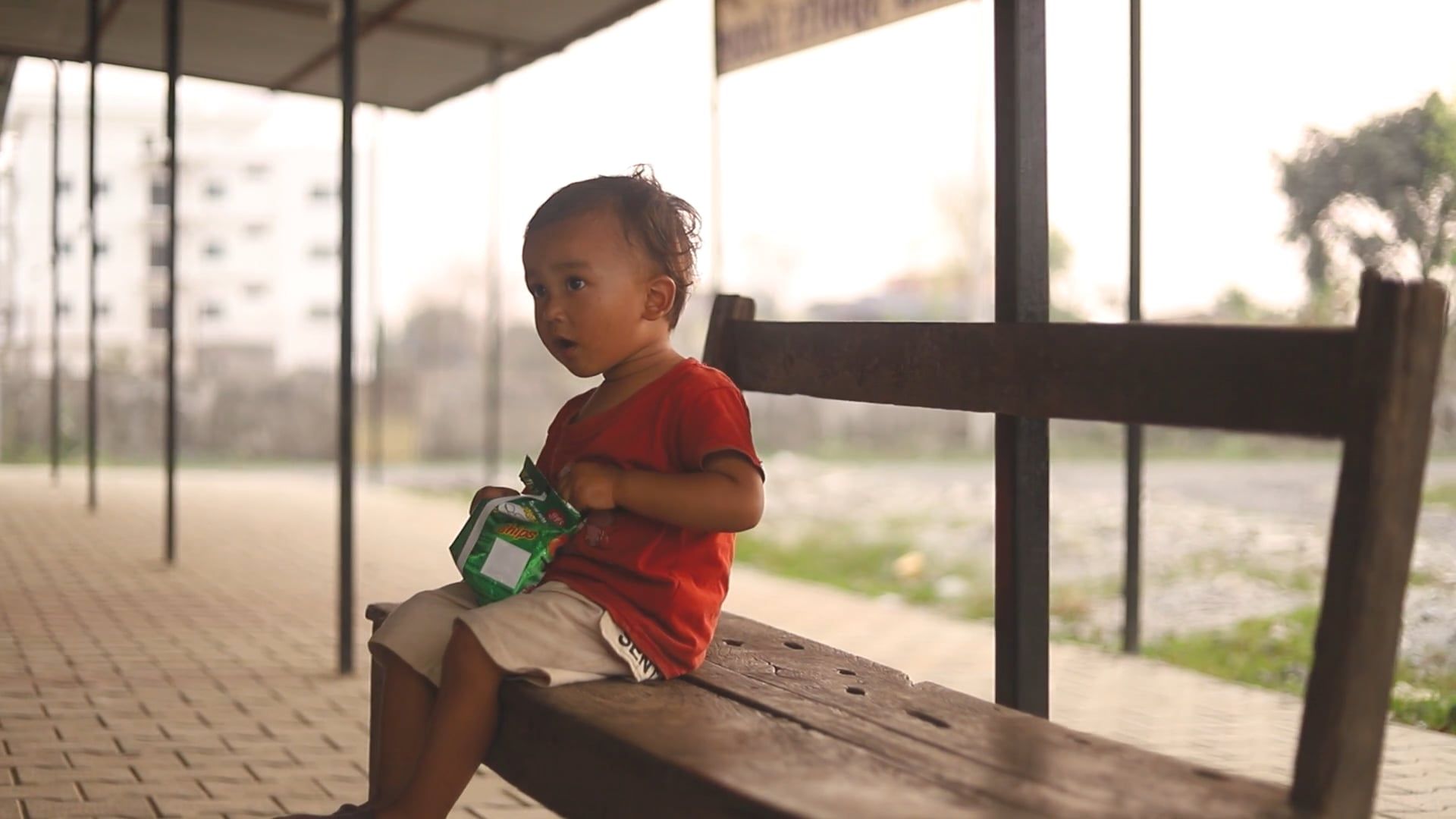A Child Sitting on a Wooden Bench Eating Snacks Free Stock Video ...