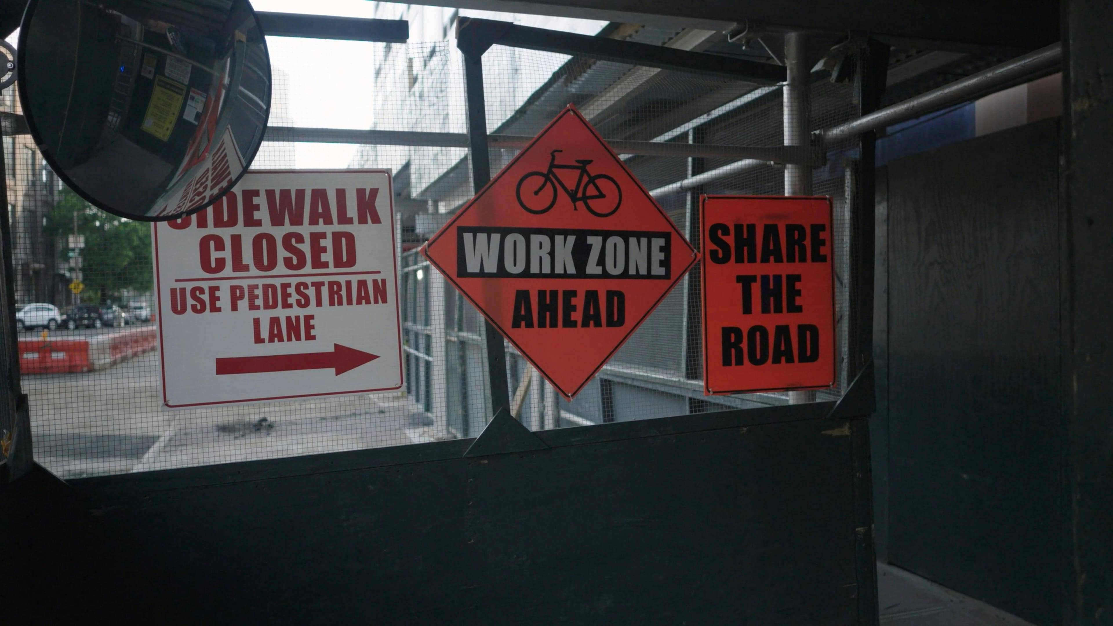 In a construction scaffold walkway, signs warn of a closed sidewalk and ...