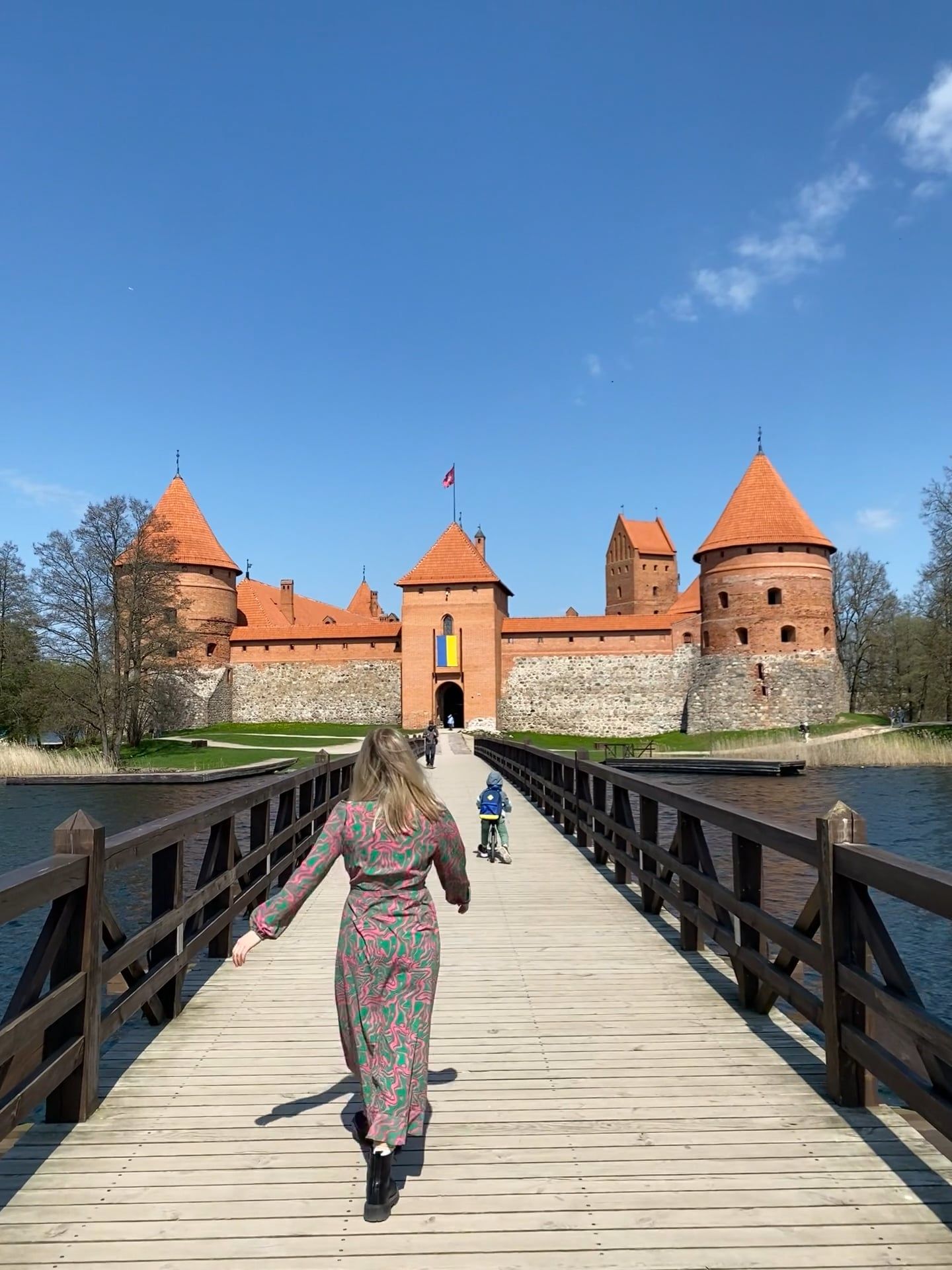 a girl walks along the bridge in front of an ancient red brick castle ...