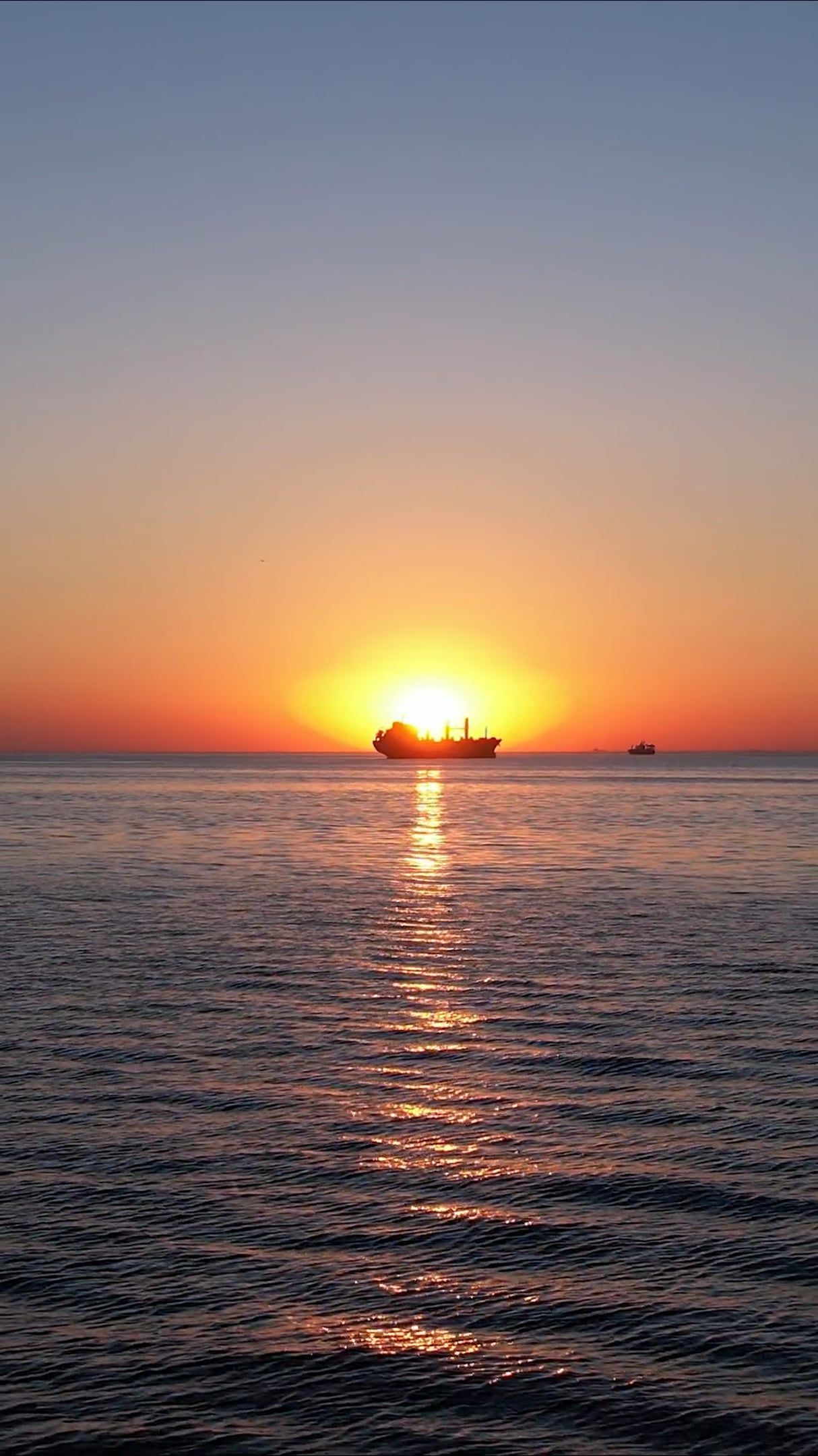 The sun setting over the ocean with a ship in the distance Free Stock ...