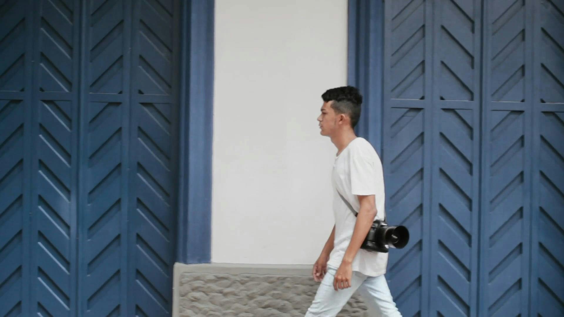 Man Walking Along The Sidewalk Carrying A Camera · Free Stock Video