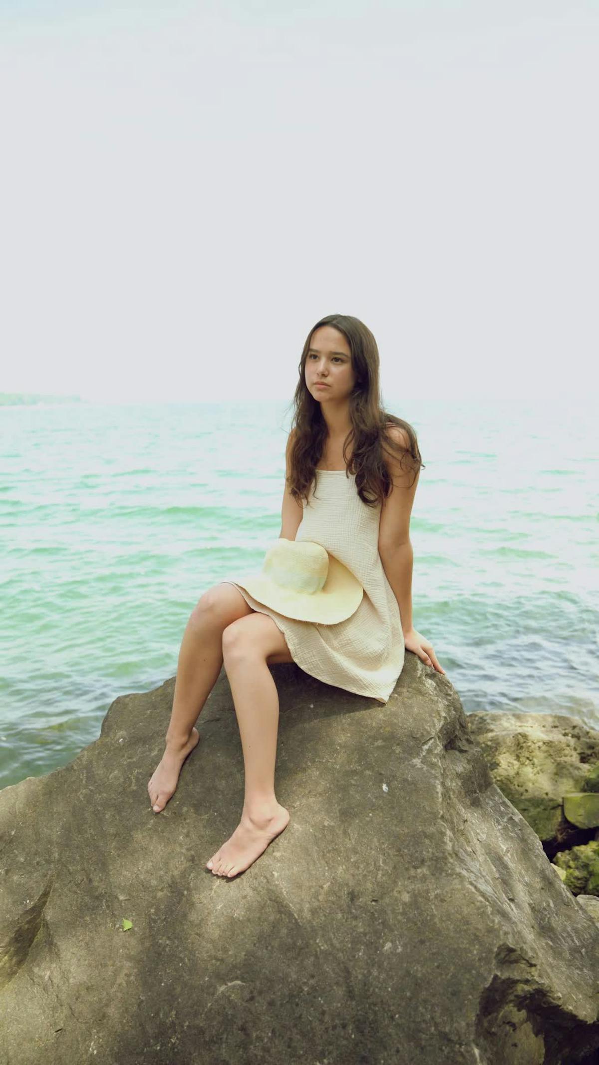 A Woman In A Black One Piece Swimsuit Sitting On A Rock Free Stock
