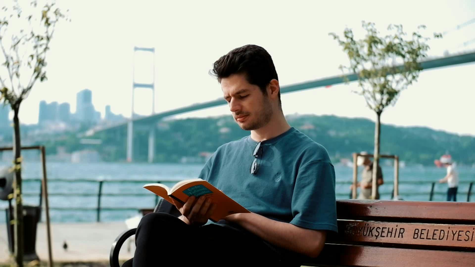 A man reading a book on a bench in front of a bridge Free Stock Video ...