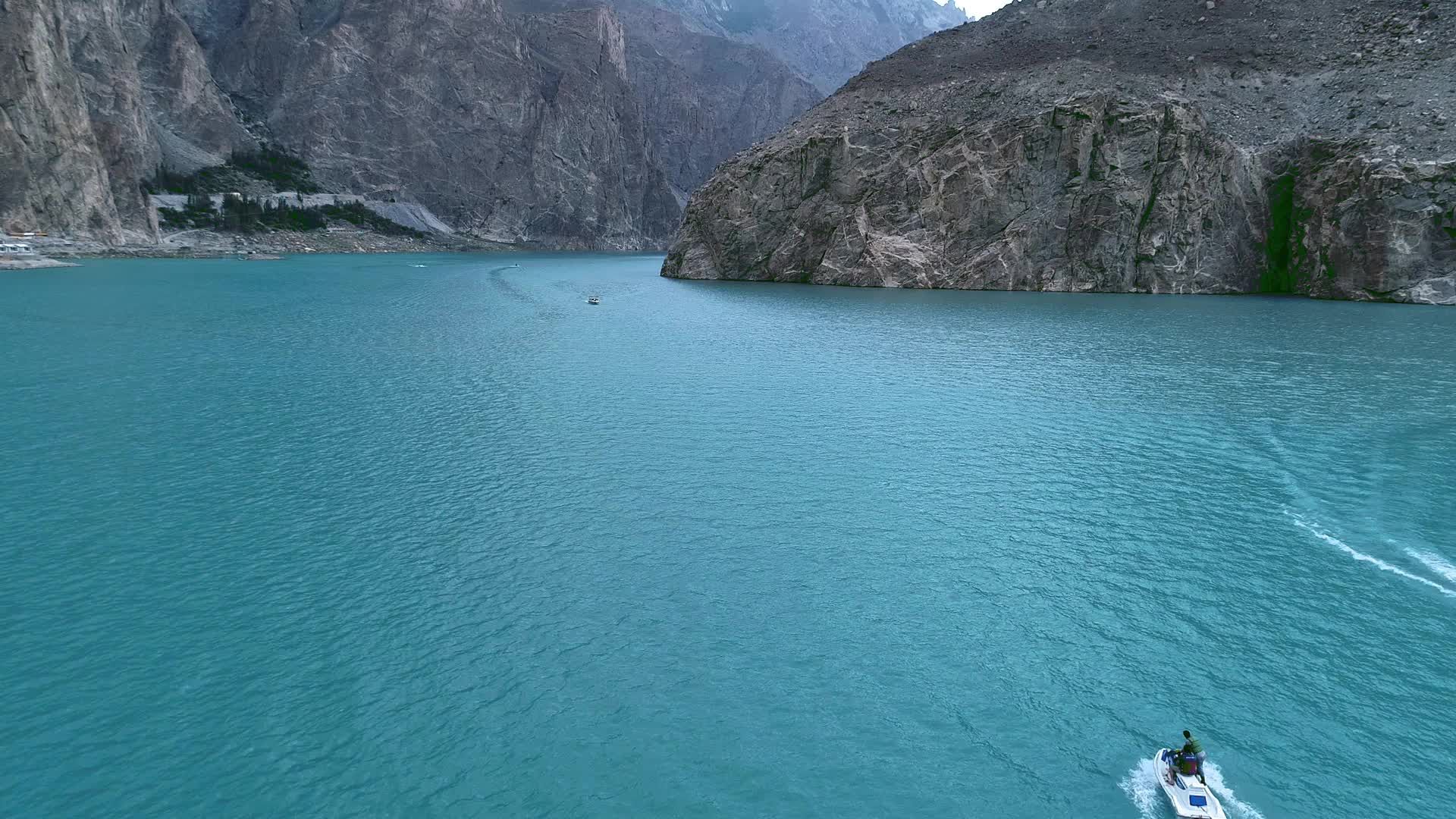 Drone flight over the Hunza valley, a long blue river below with boats ...