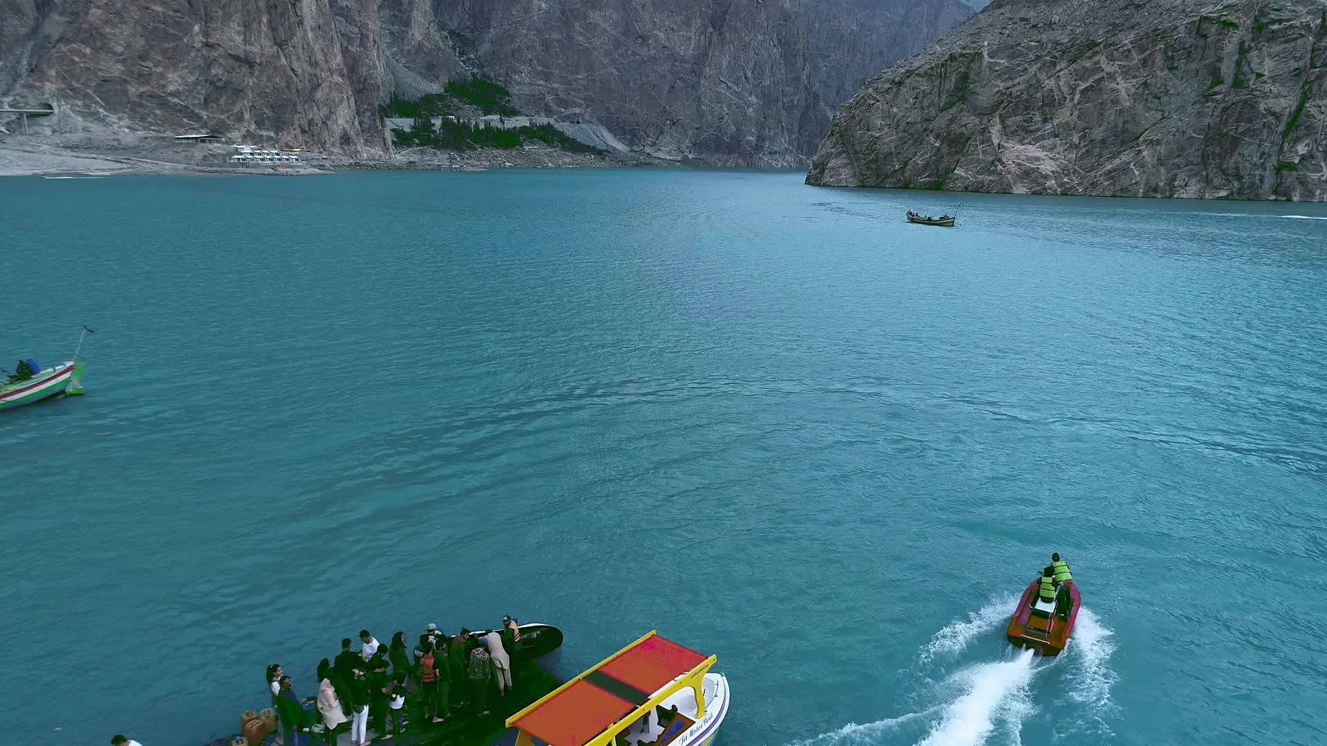 Drone flight over the Hunza valley, a long blue river below with boats ...