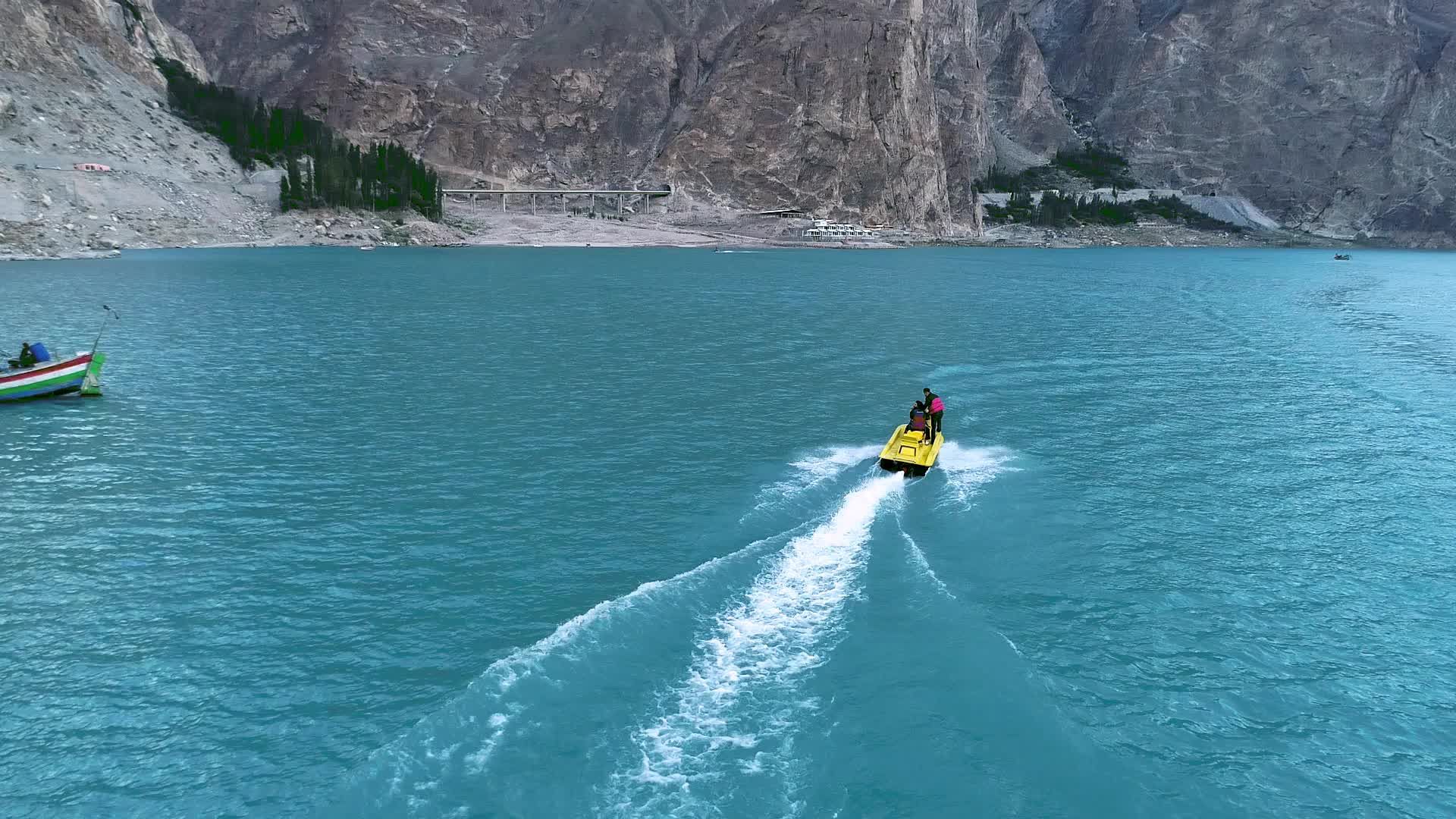 Drone flight over the Hunza valley, a long blue river below with boats ...