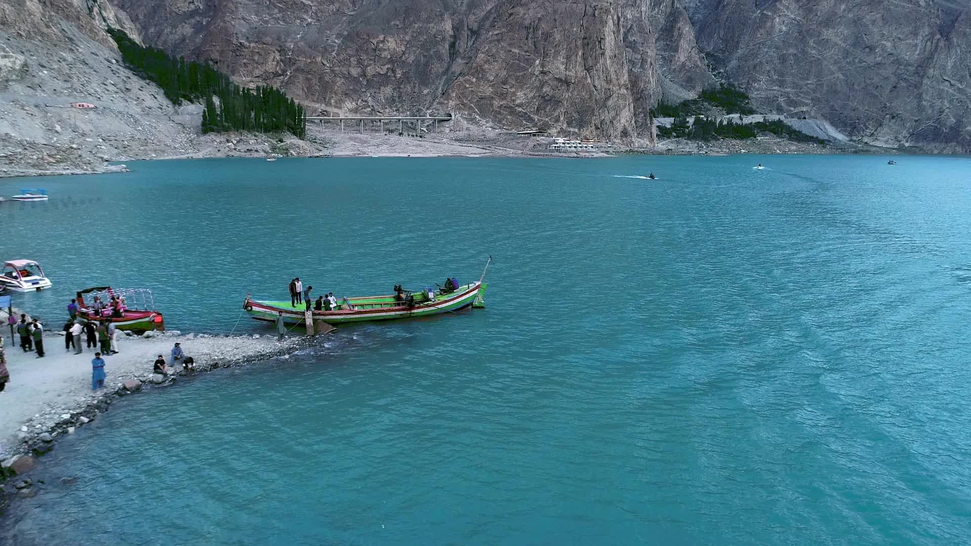 Drone flight over the Hunza valley, a long blue river below with boats ...
