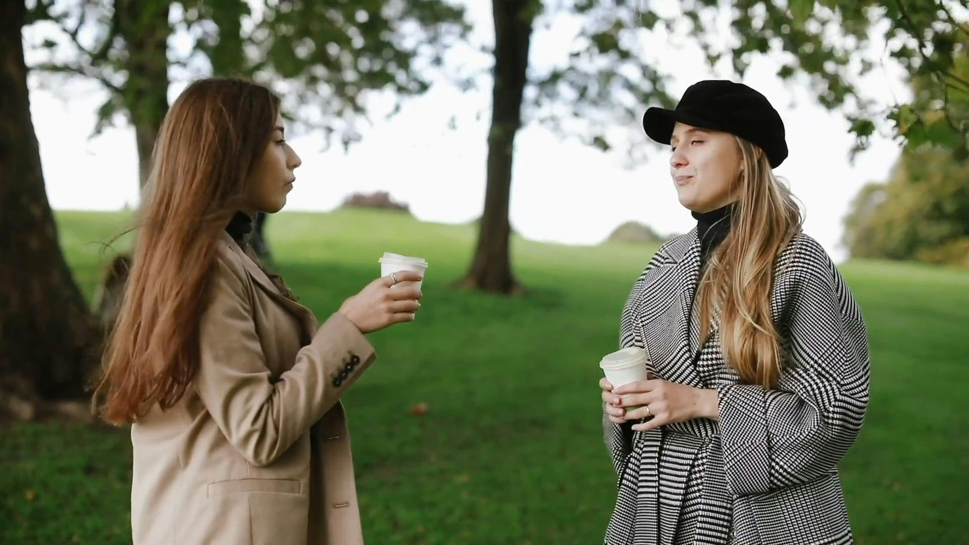 Two Standing Women Talking In The Park While Having Coffee · Free Stock ...