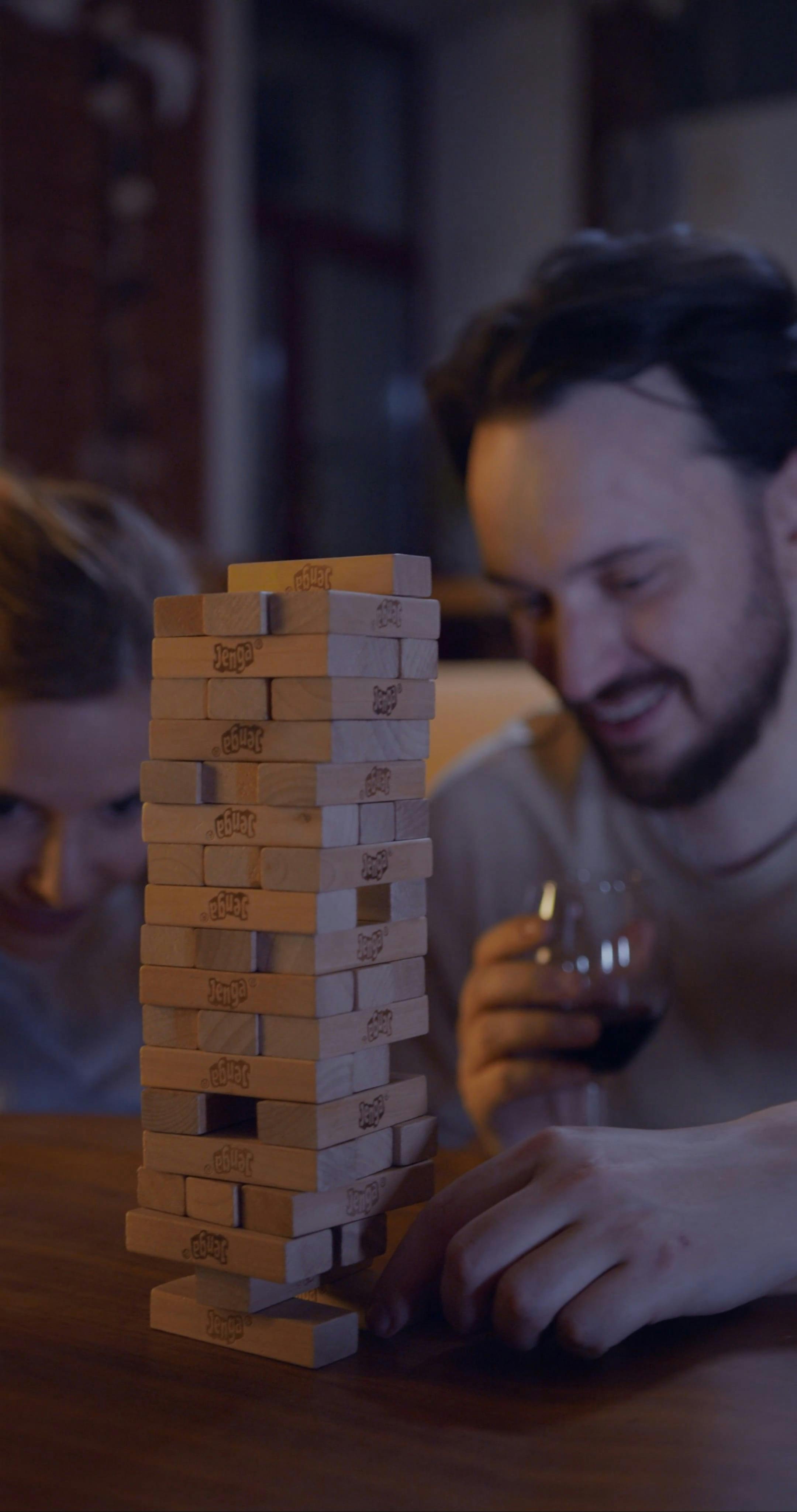 A Couple Playing A Game Of Jenga At Home While Having A Glass Of Wine ...
