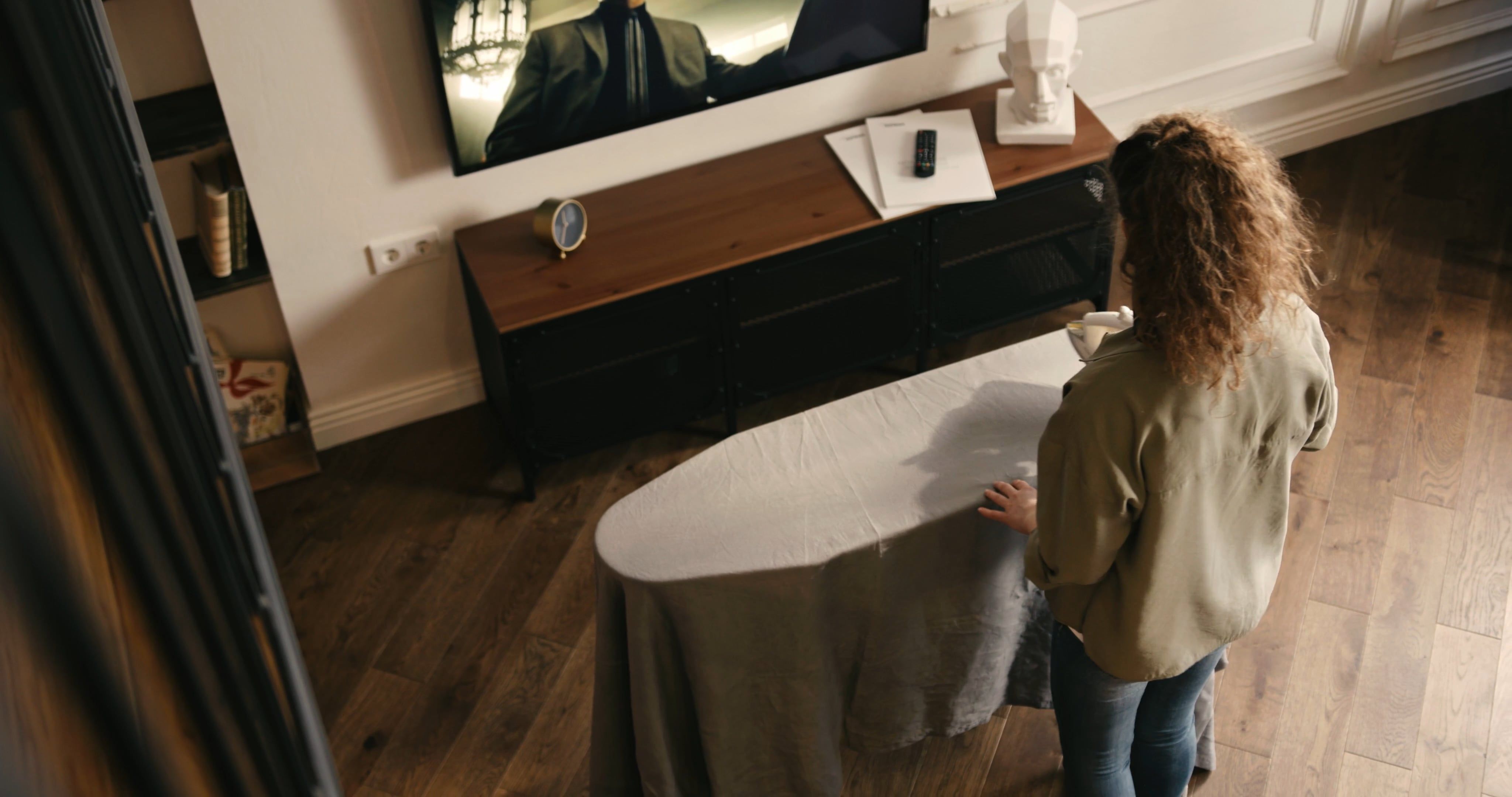A Woman Flat Ironing A Table Cloth While Watching A Television · Free ...