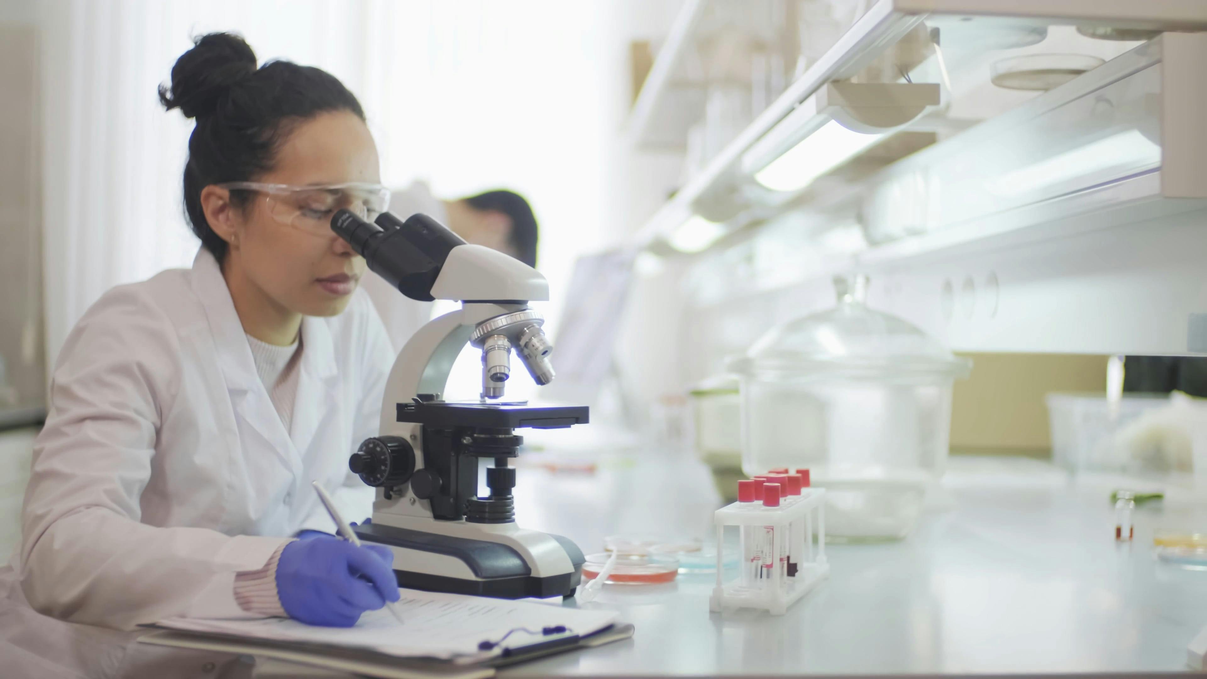 A Woman Writing while Looking Through the Microscope · Free Stock Video