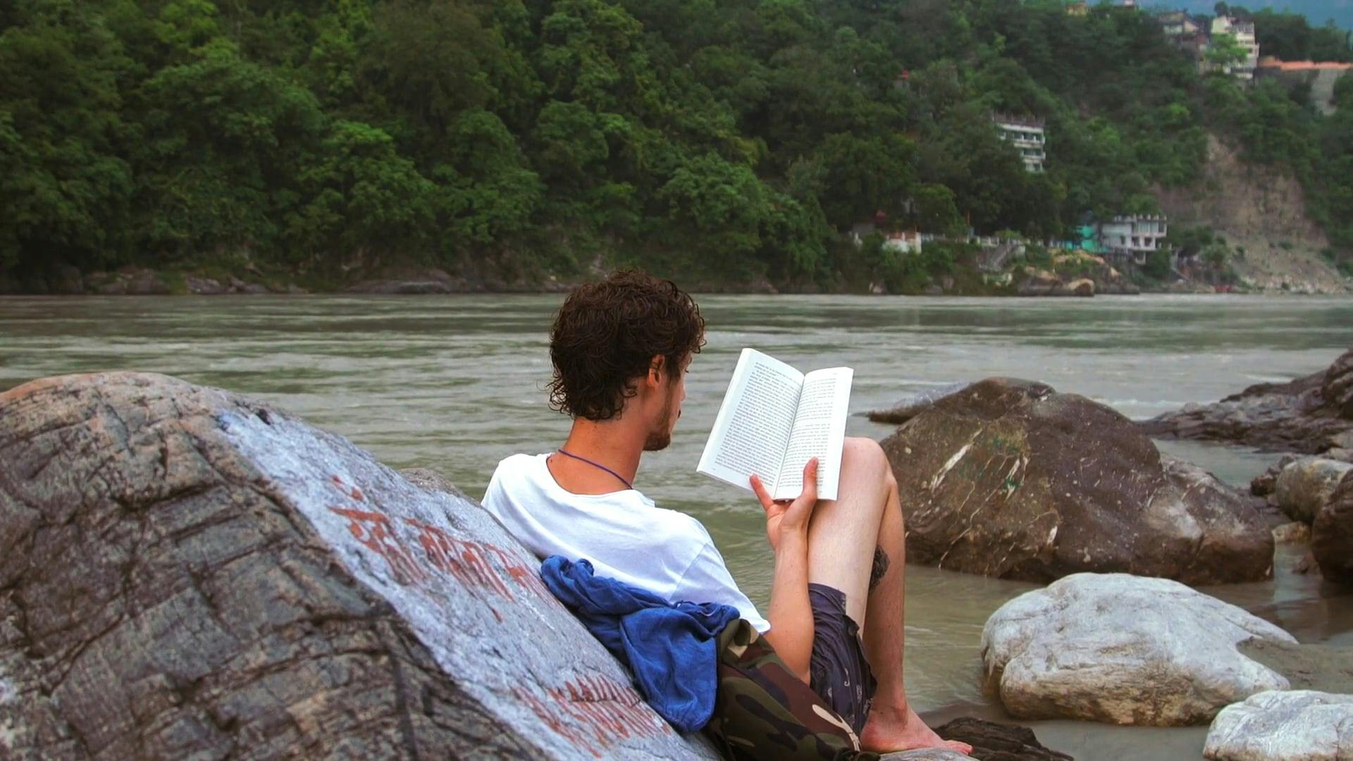 Man Sitting On A Rock Reading A Book Near The River · Free Stock Video