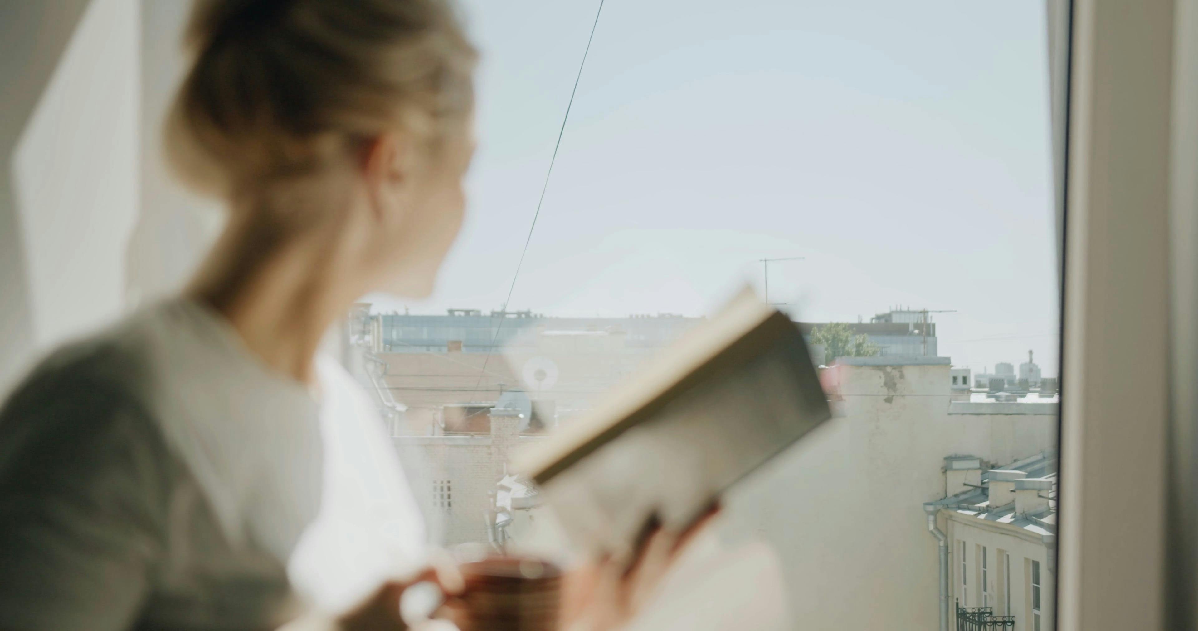 A woman reading a book while looking out the window Free Stock Video ...