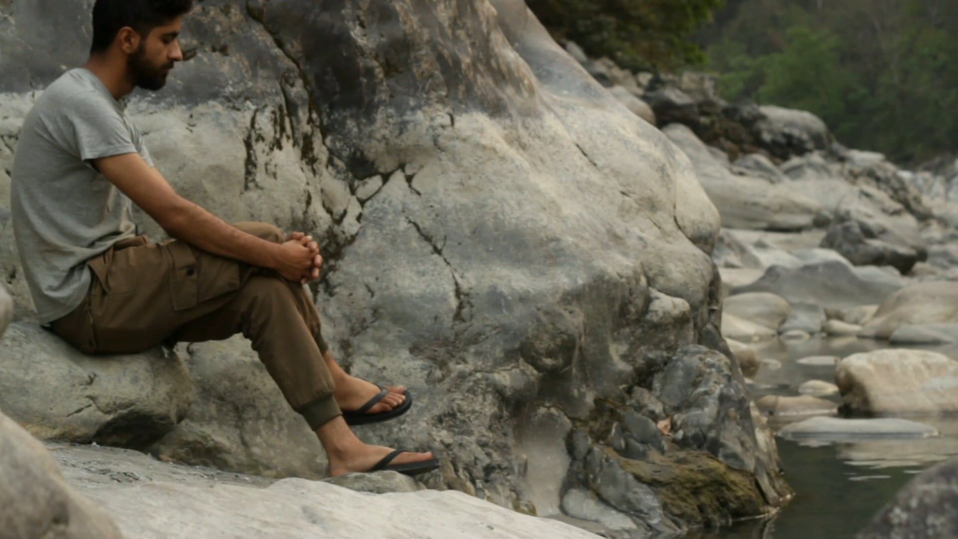 Man Sitting on a Rock Throwing His Slippers in the River Free Stock ...