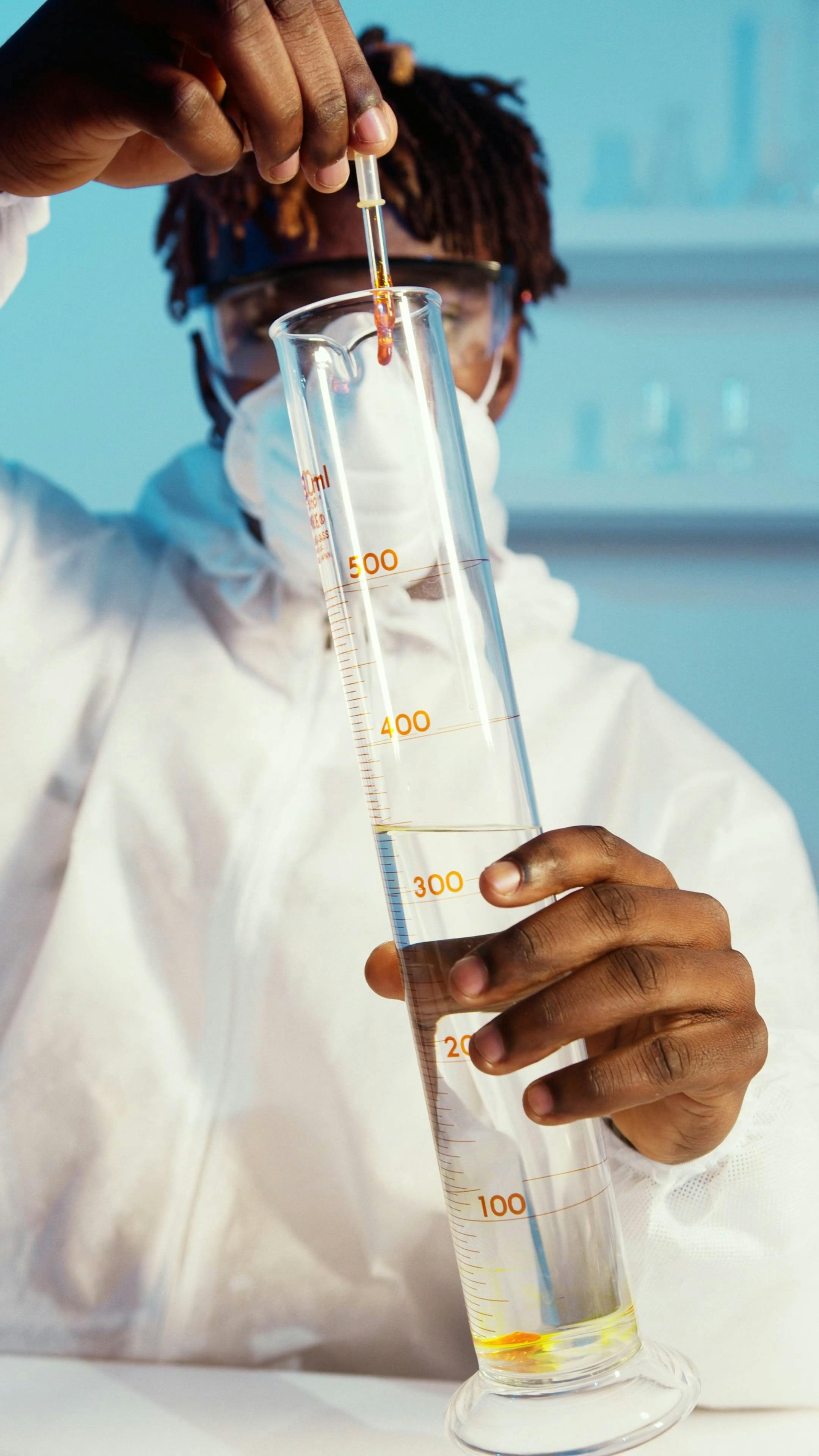 A Man Dropping an Orange Liquid into a Graduated Cylinder Filled with ...