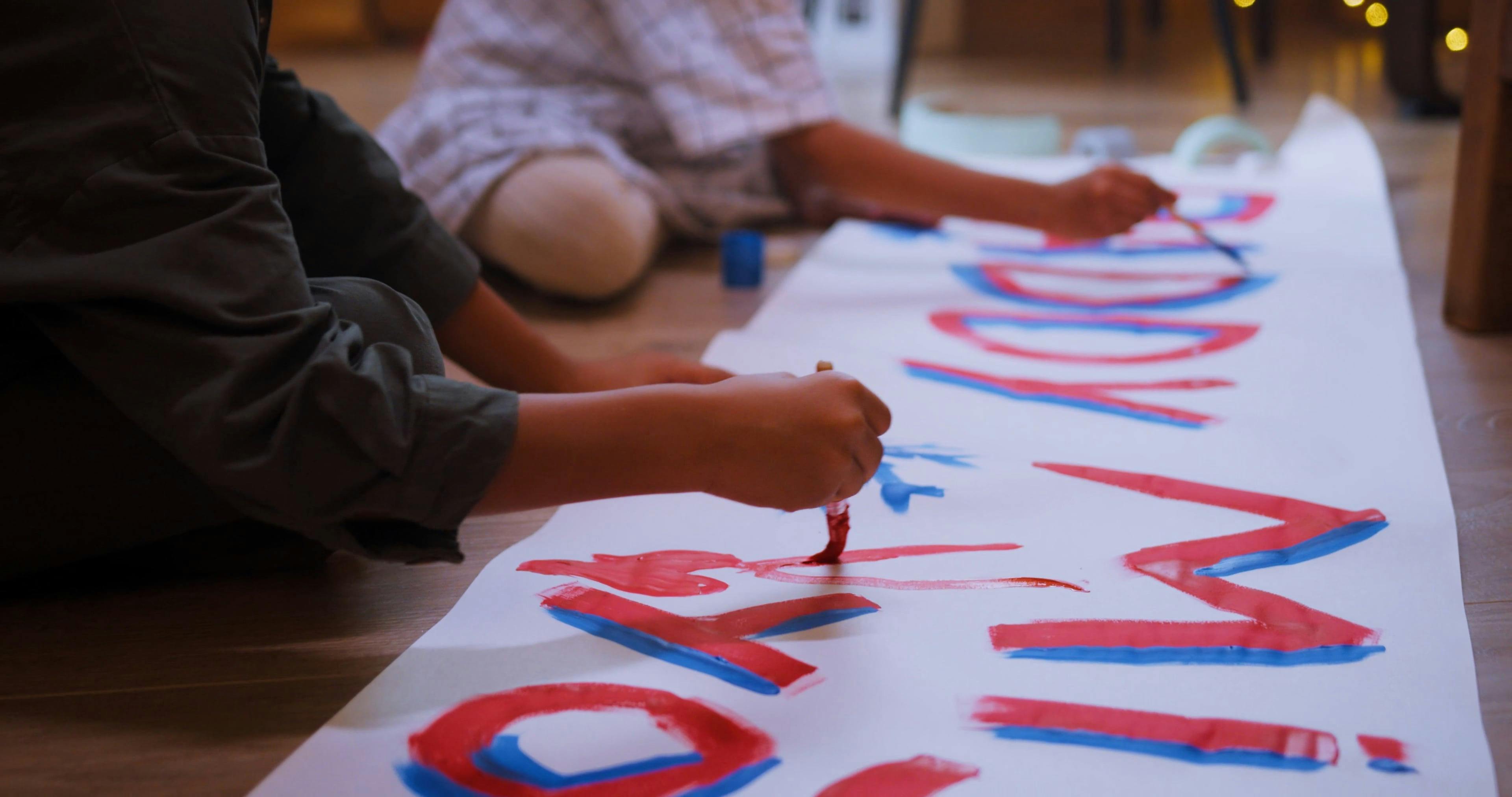 Two Kids Writing Text on White Banner Using Paint and Brushes · Free ...