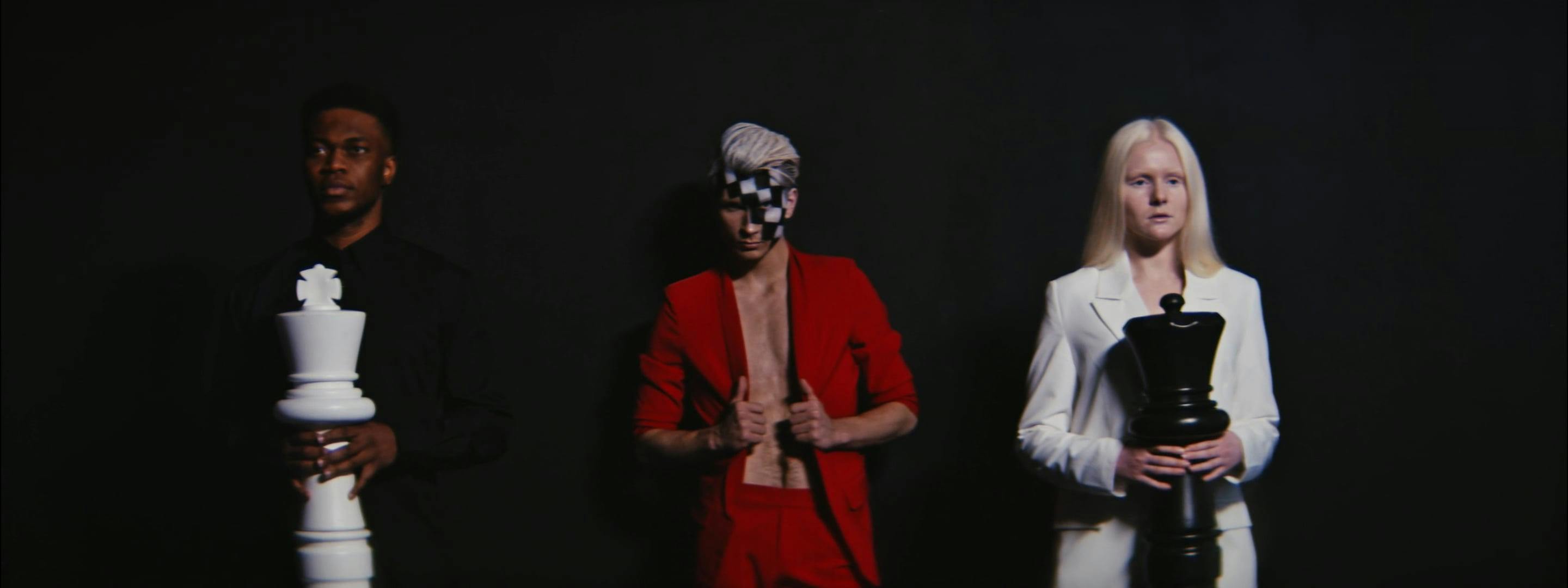 A Man with Face Paint Dancing Between Two People Holding Big Chess ...