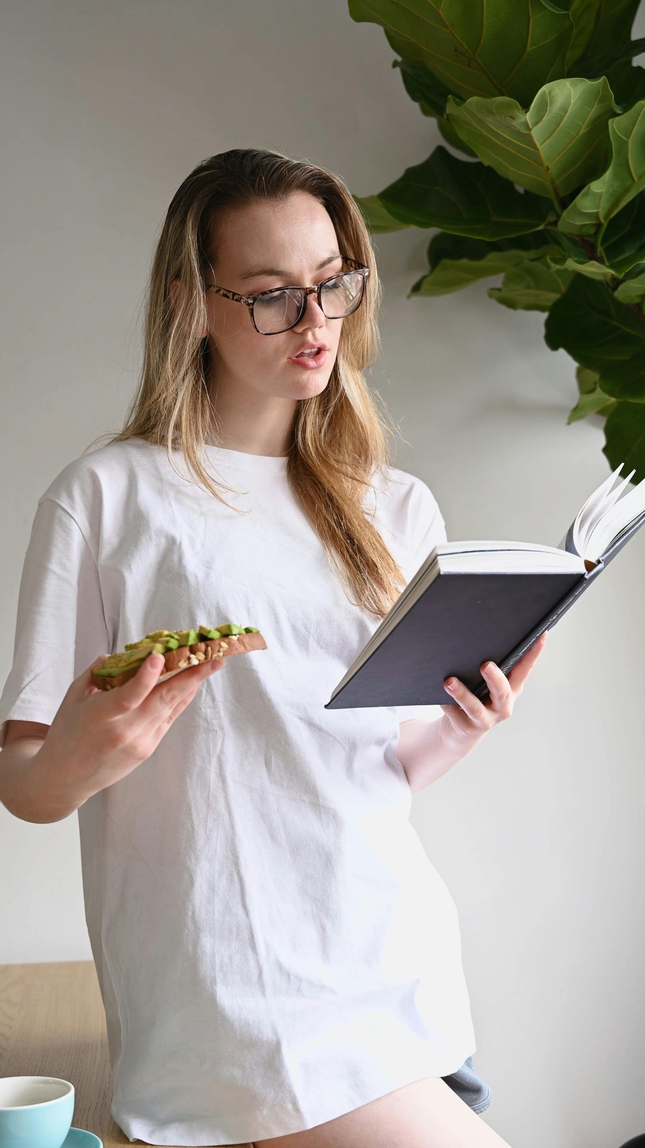 Woman Reading a Book while Eating an Avocado Toast · Free Stock Video