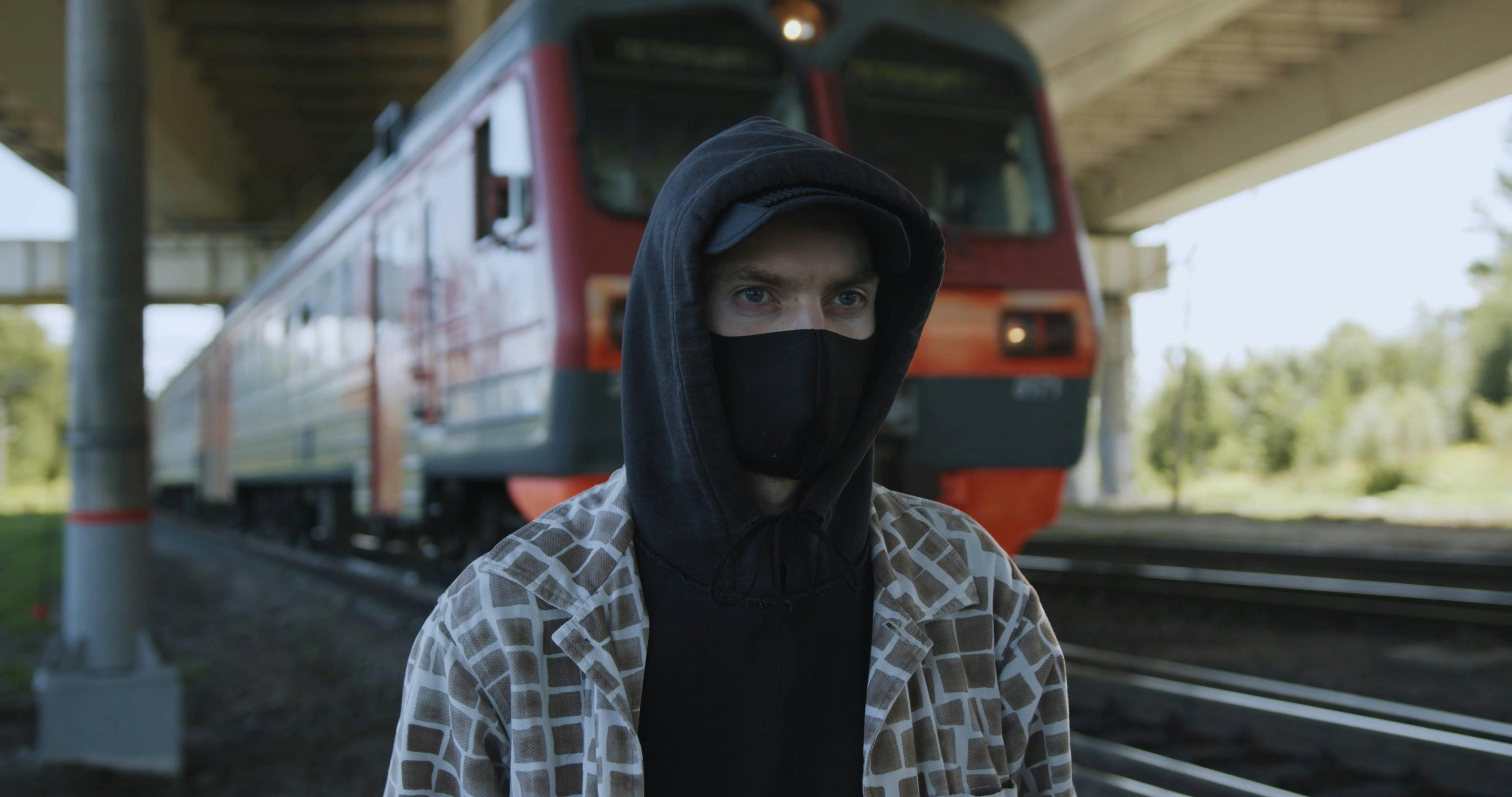 A Man Wearing a Mask and Hood Posing beside a Moving Train Free Stock ...