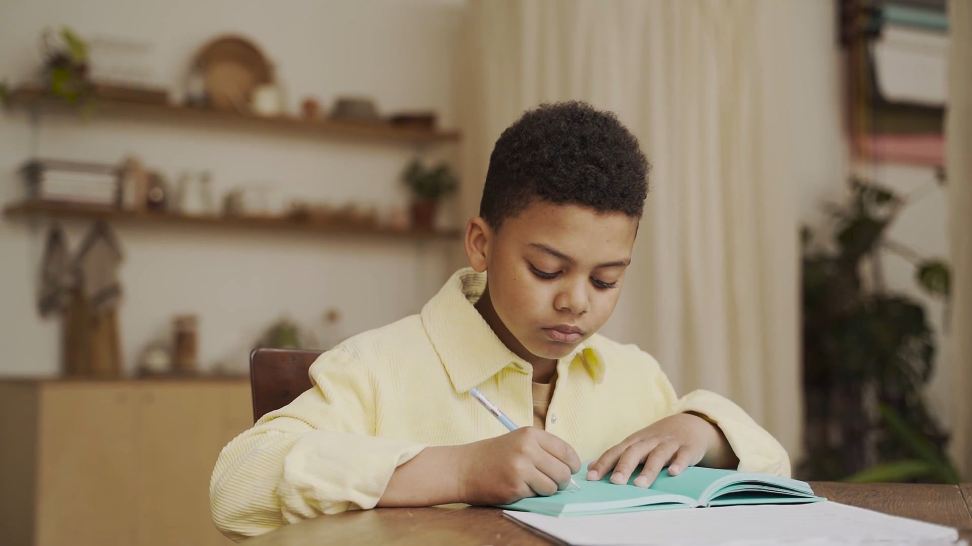 A Boy Writing on His Notebook While Smiling in the Camera Free Stock ...