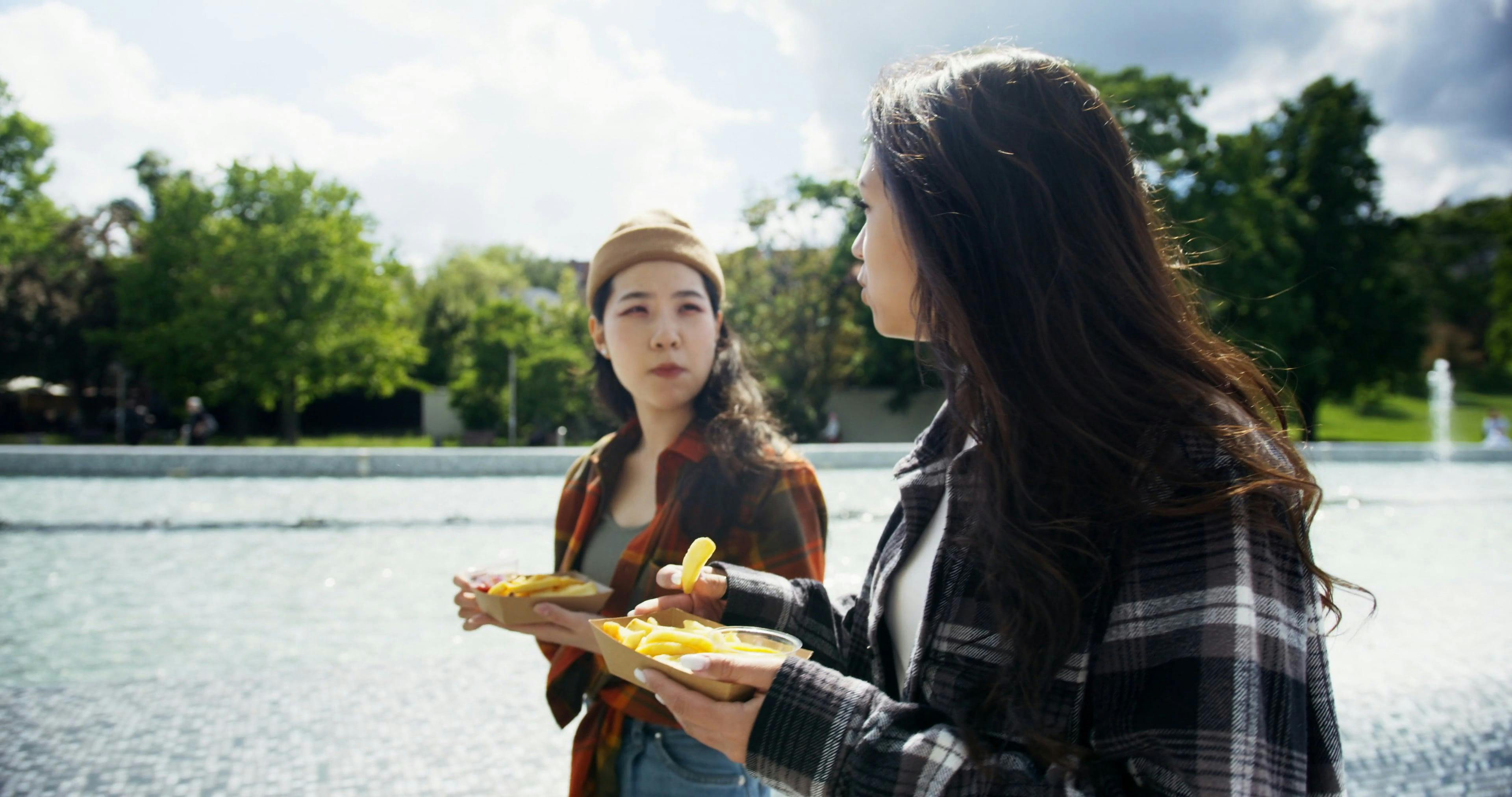 Two Friends Eating French Fries while Walking Beside the Fountain Free ...