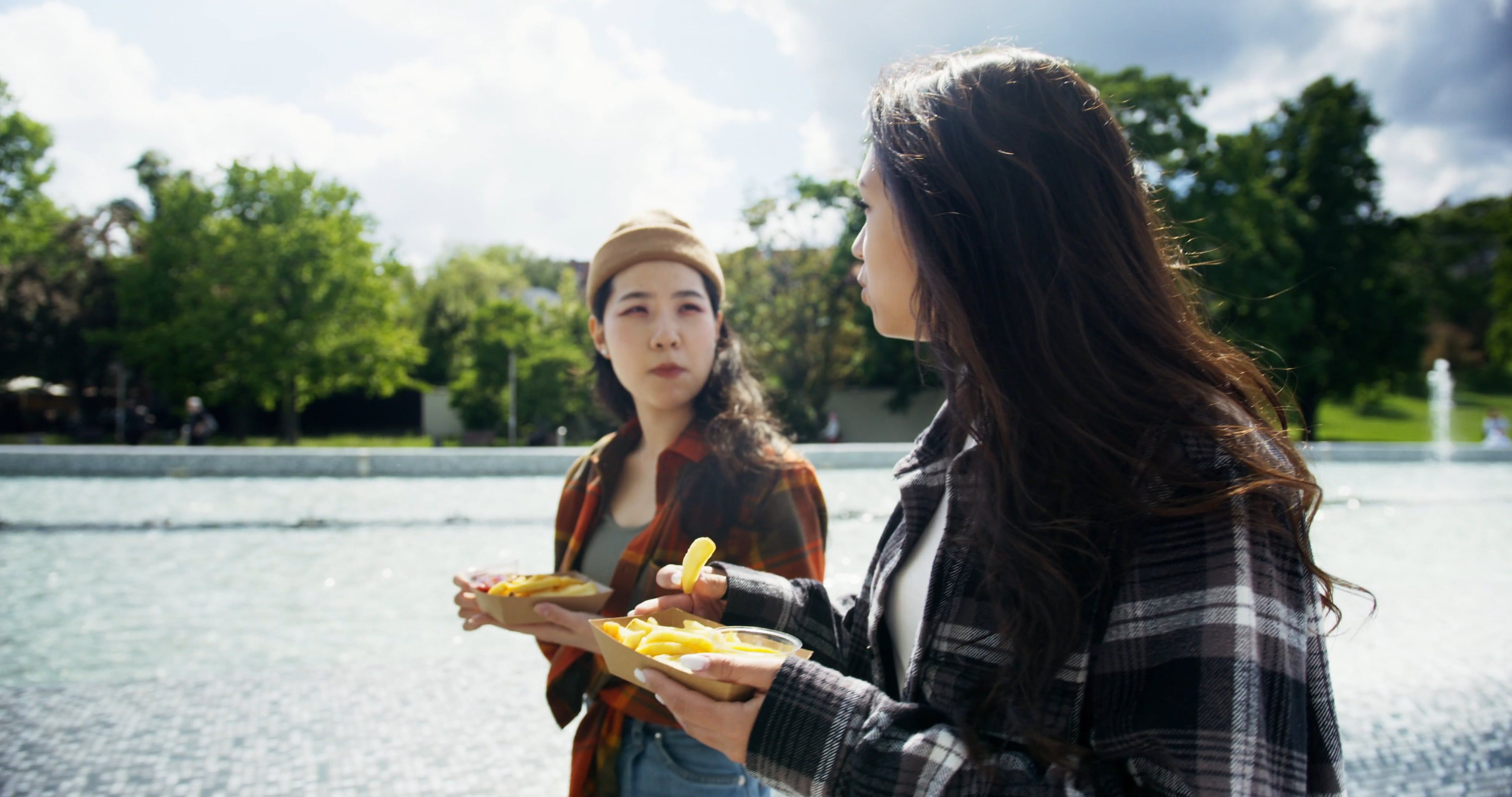 Two Friends Eating French Fries while Walking Beside the Fountain ...