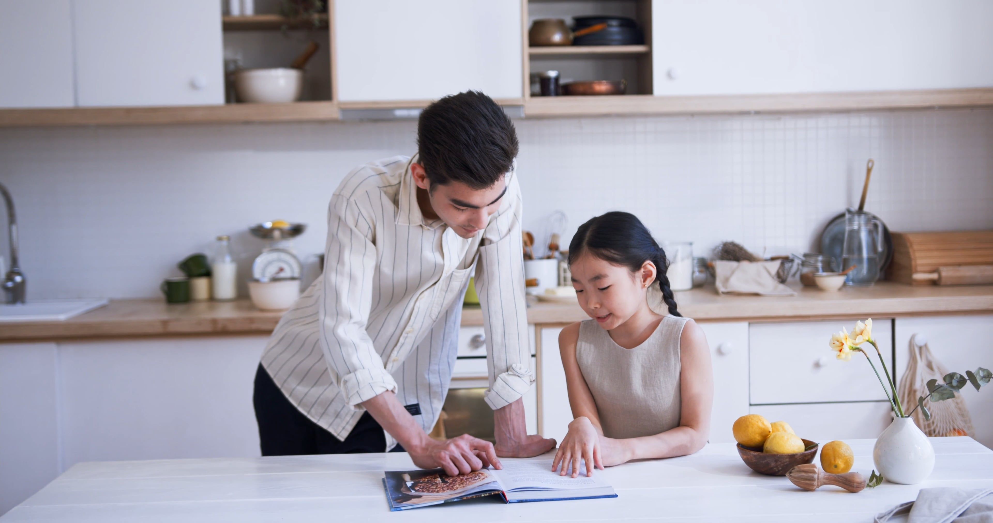 A Man Reading a Cookbook with his Daughter in a Kitchen Free Stock ...