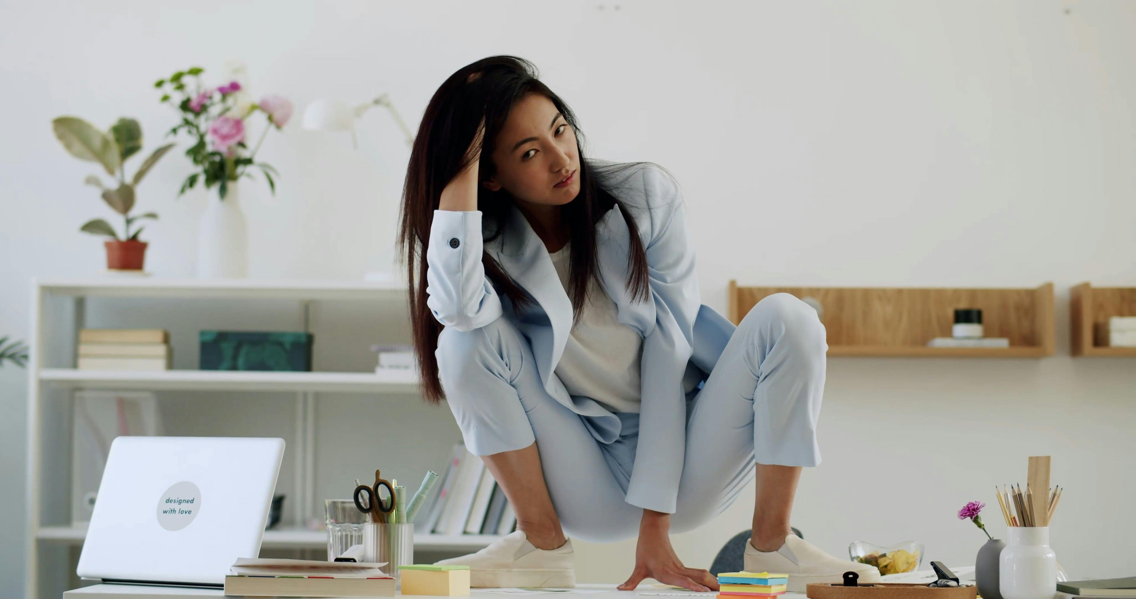 A Woman in Corporate Attire Squatting on a Desk and Playing with her ...